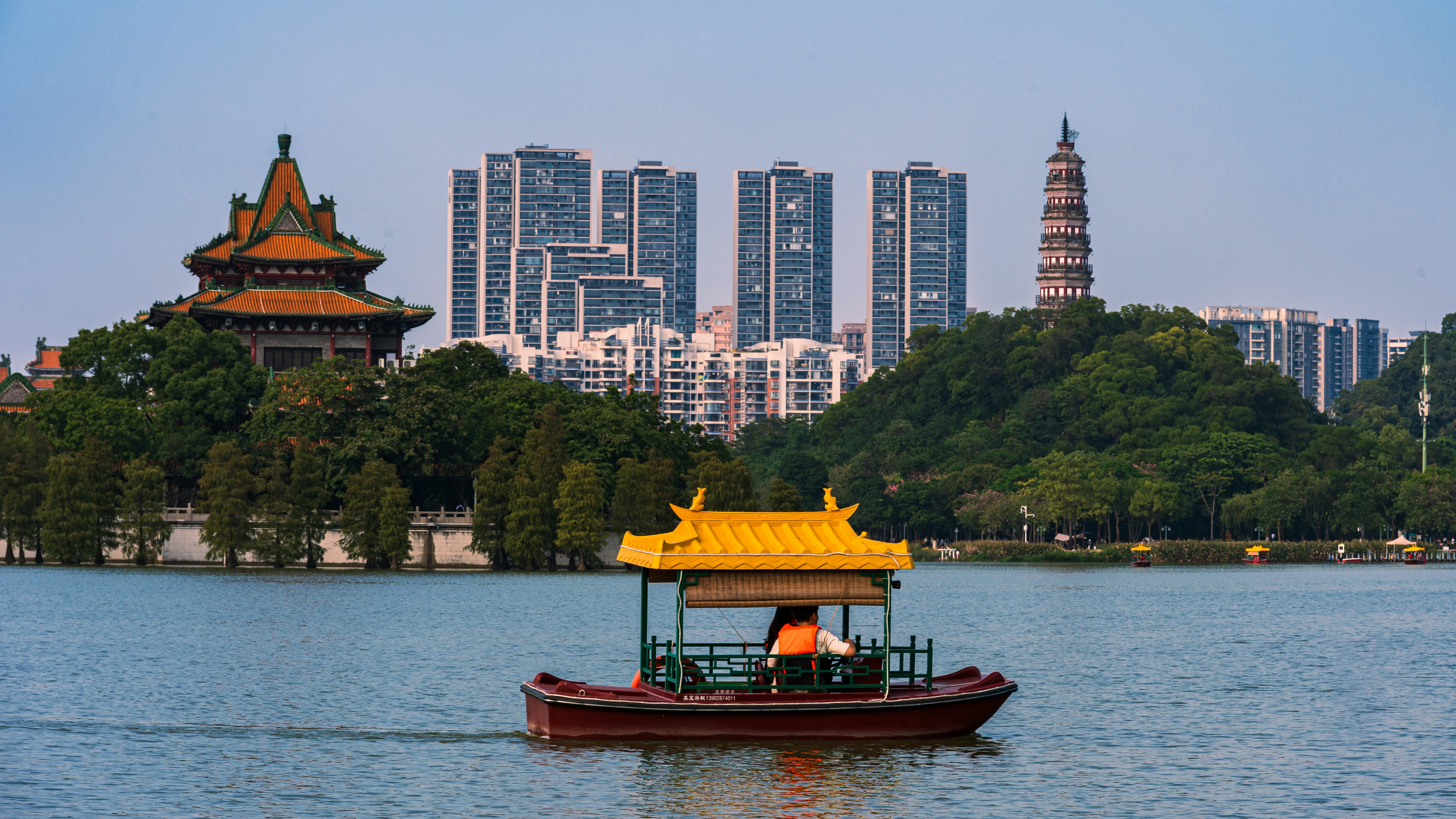 Yellow-Canopy Boat Crossing a Quiet Lake Before a City of Pagodas and Towers