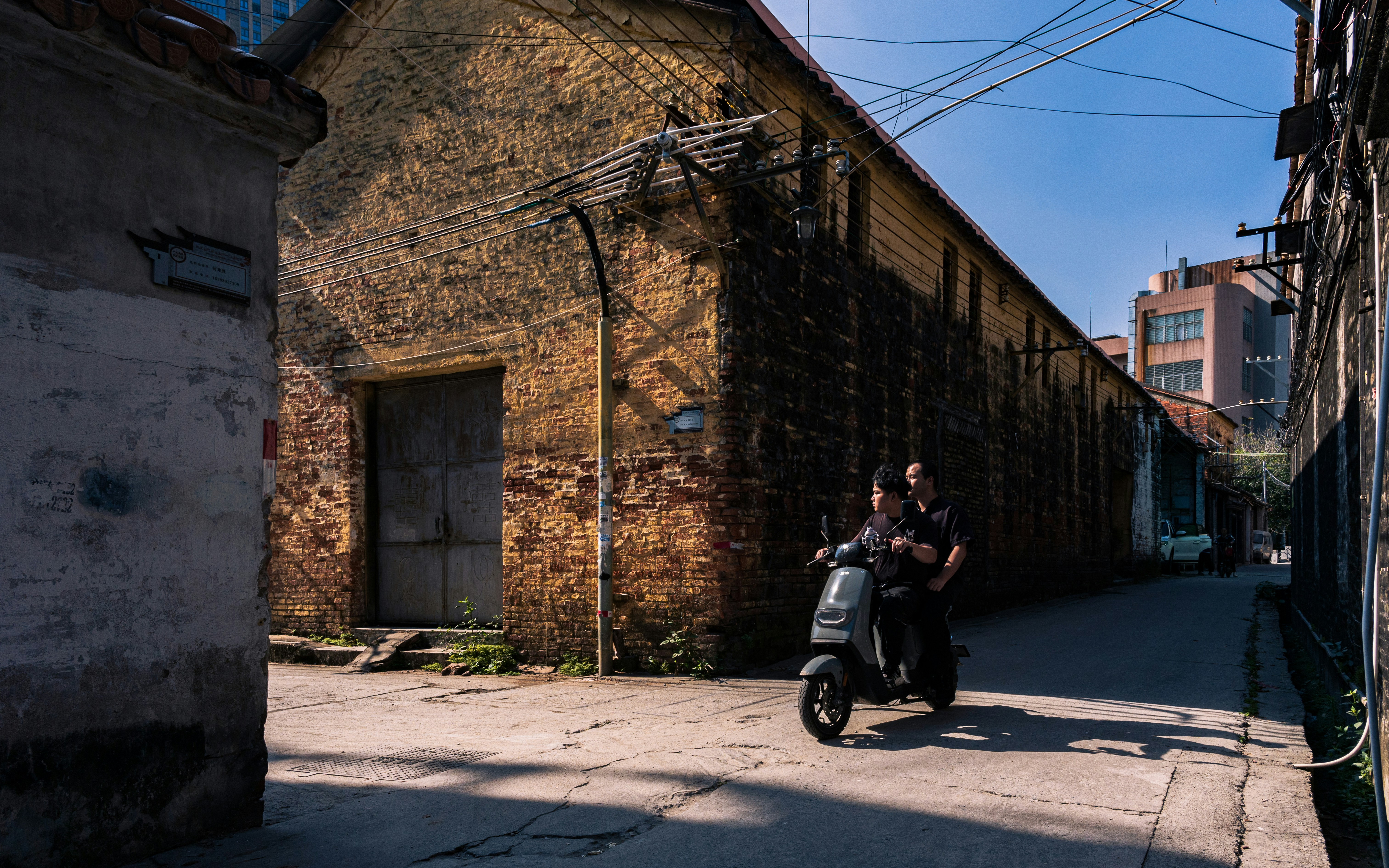 Sunlit Alley Duo: A Scooter Threading Through Weathered Brick