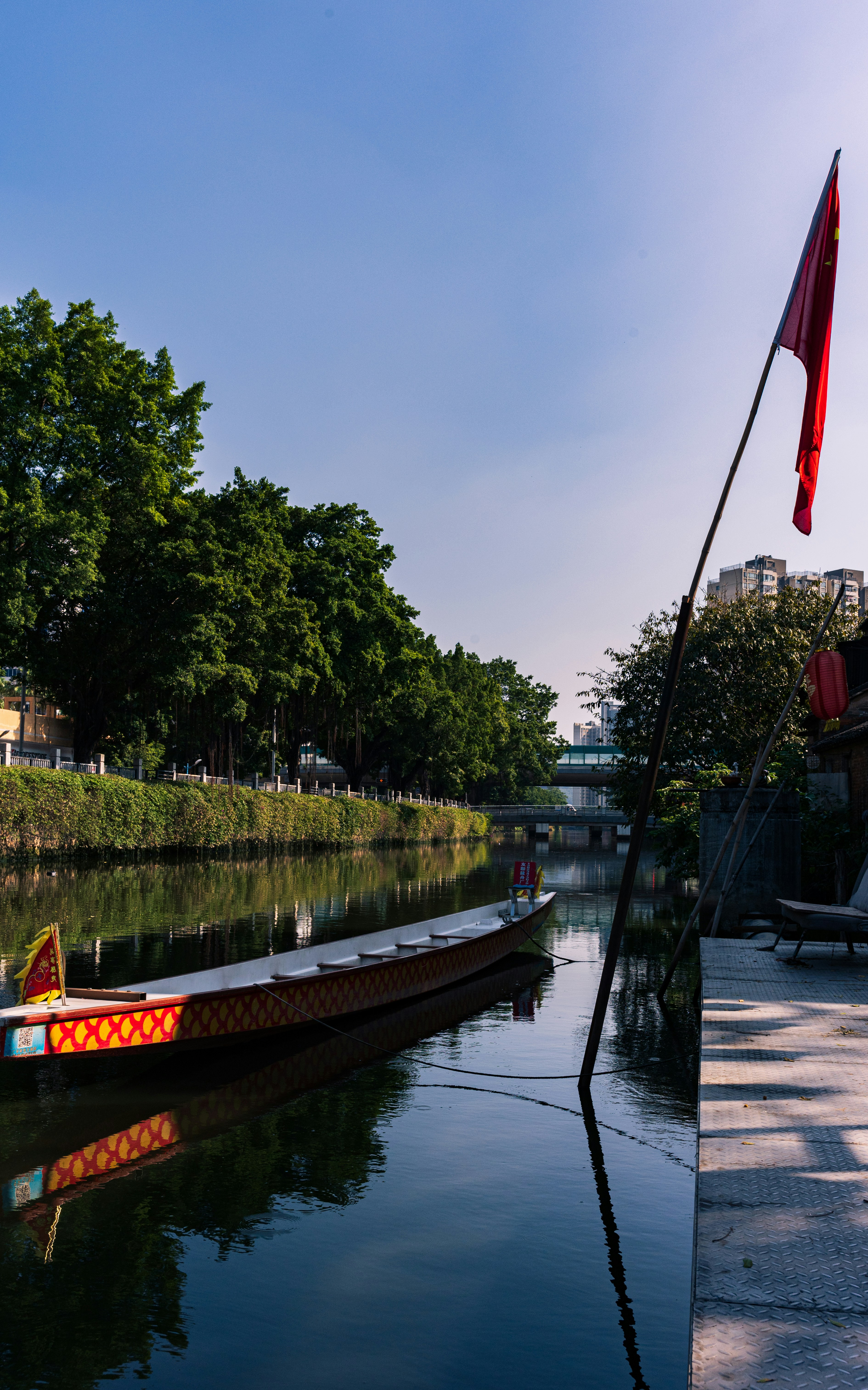 Longboat at a Quiet City Canal, Red Flag Framing the Riverside