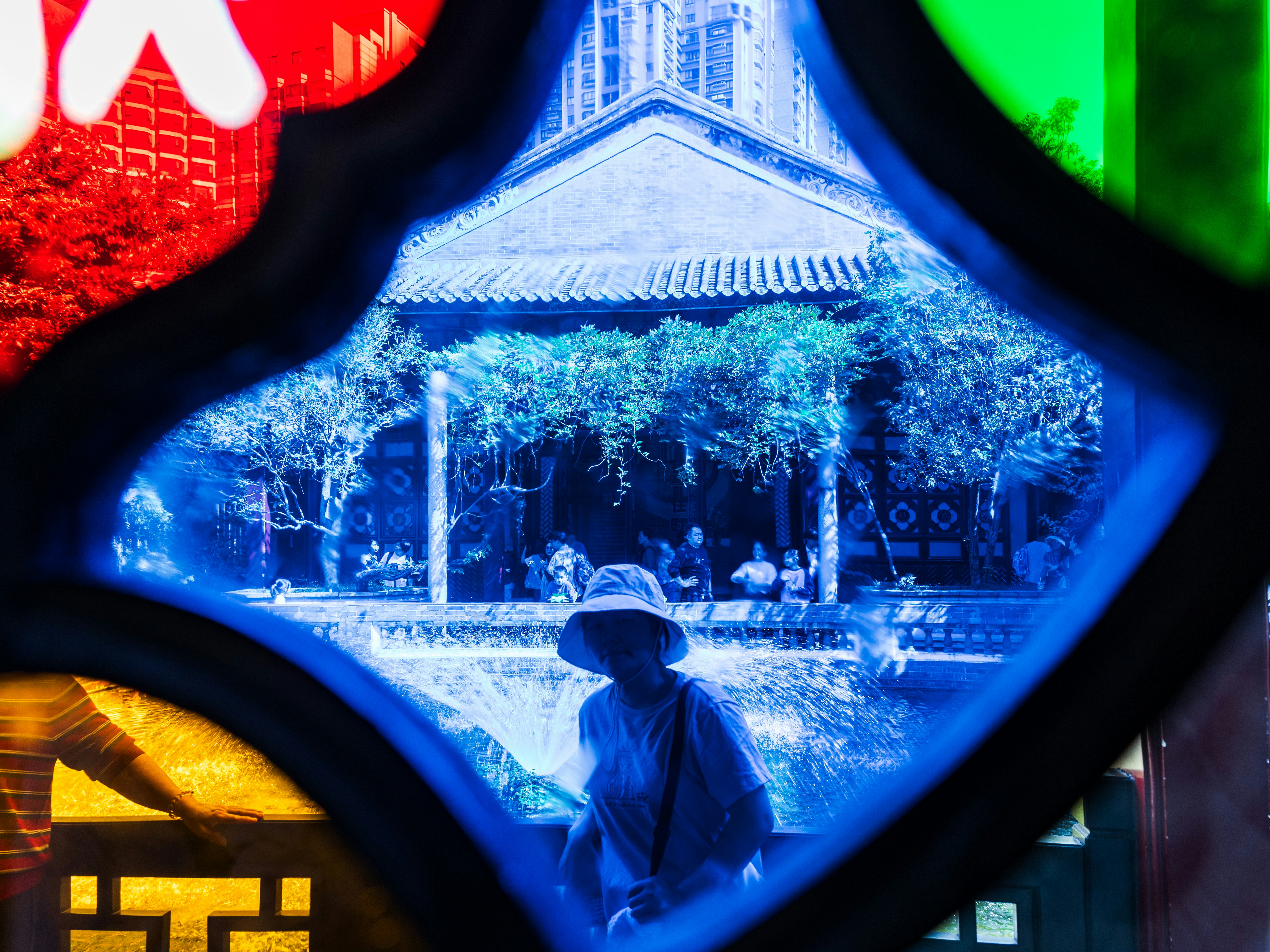 Through the Color-Sliced Frame: A Hat-Wearing Figure in a Quiet Courtyard