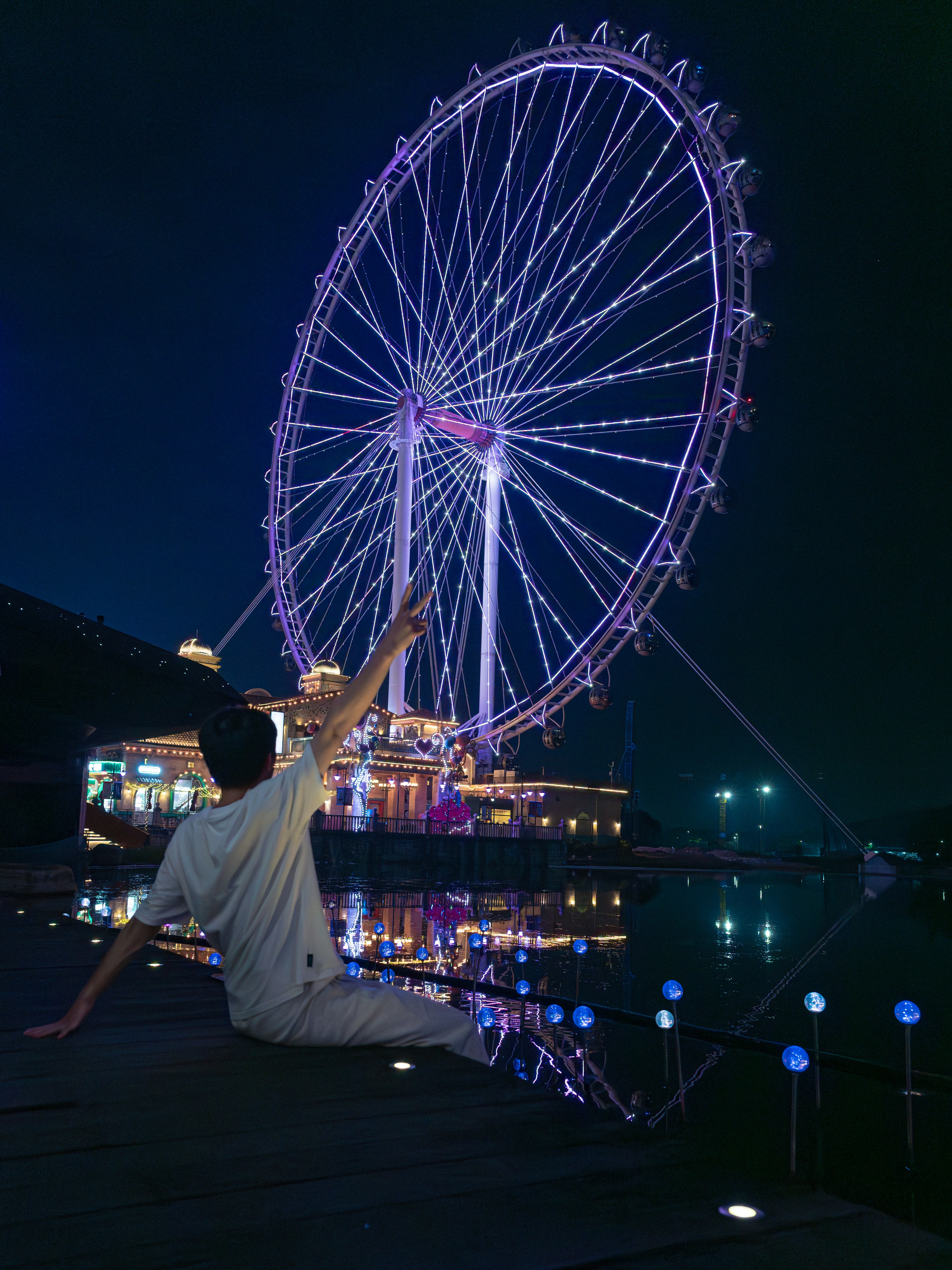 Neon Ferris Wheel Aglow Over the River: A Night Portrait by the Foreground Spectator
