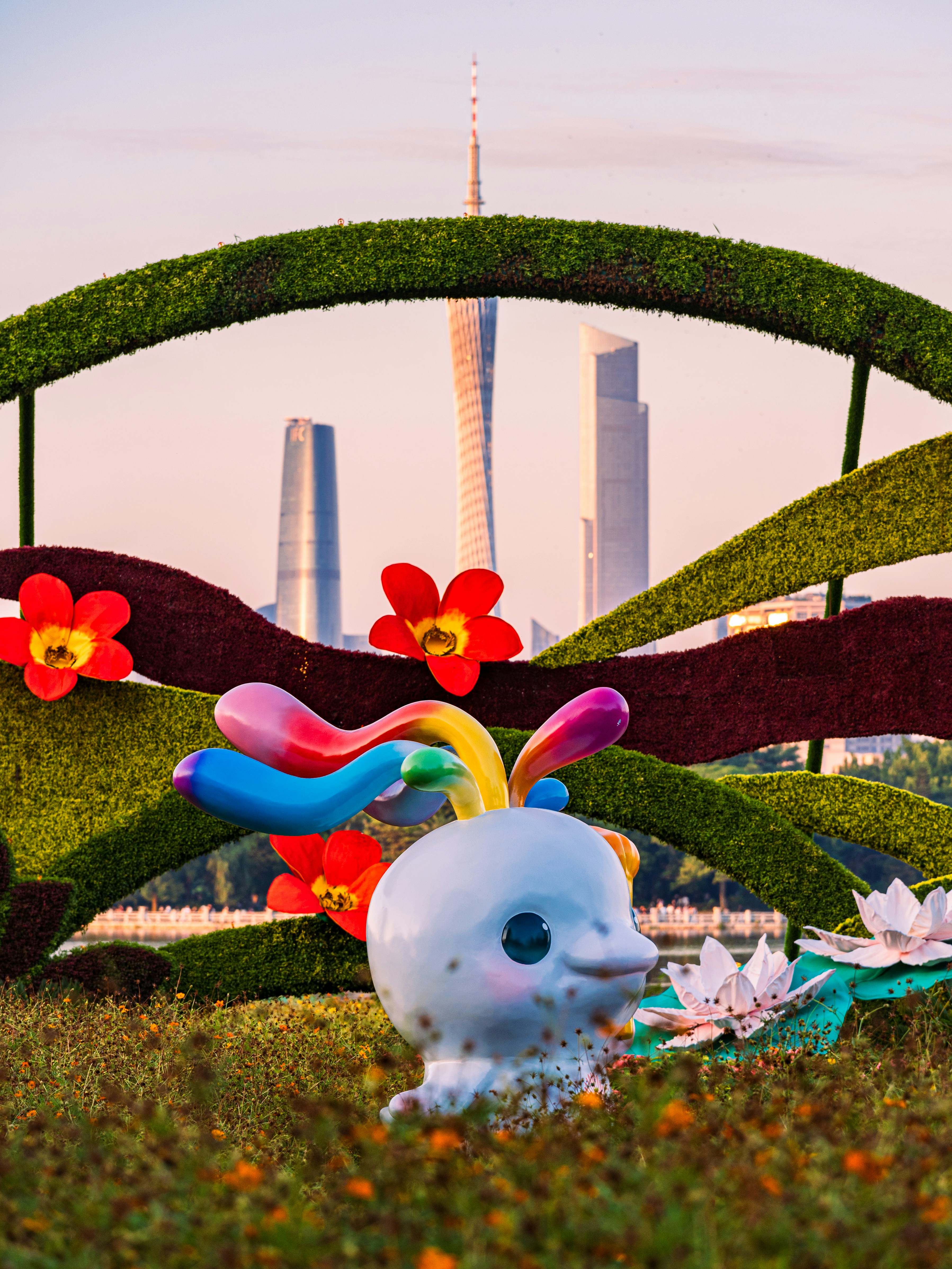 Rainbow Crest Sculpture Framed by Emerald Arches Against a Distant City Skyline