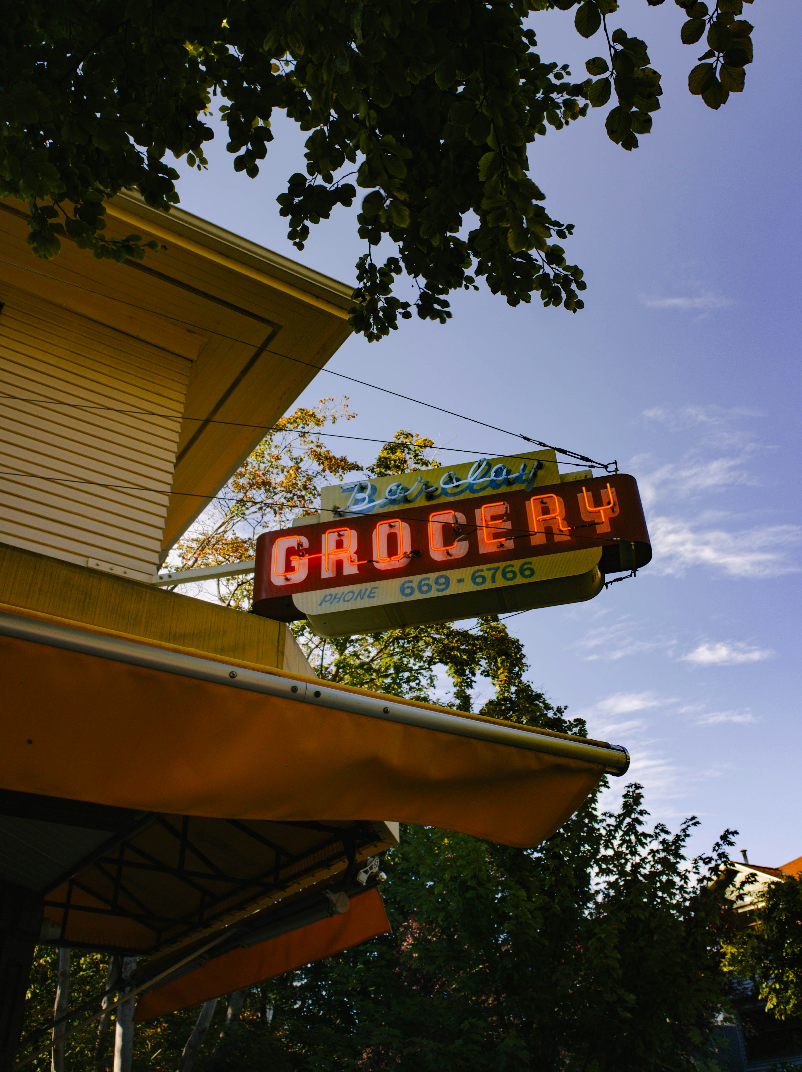 Neon Grocery Sign Under a Canary Awning Framed by Sky