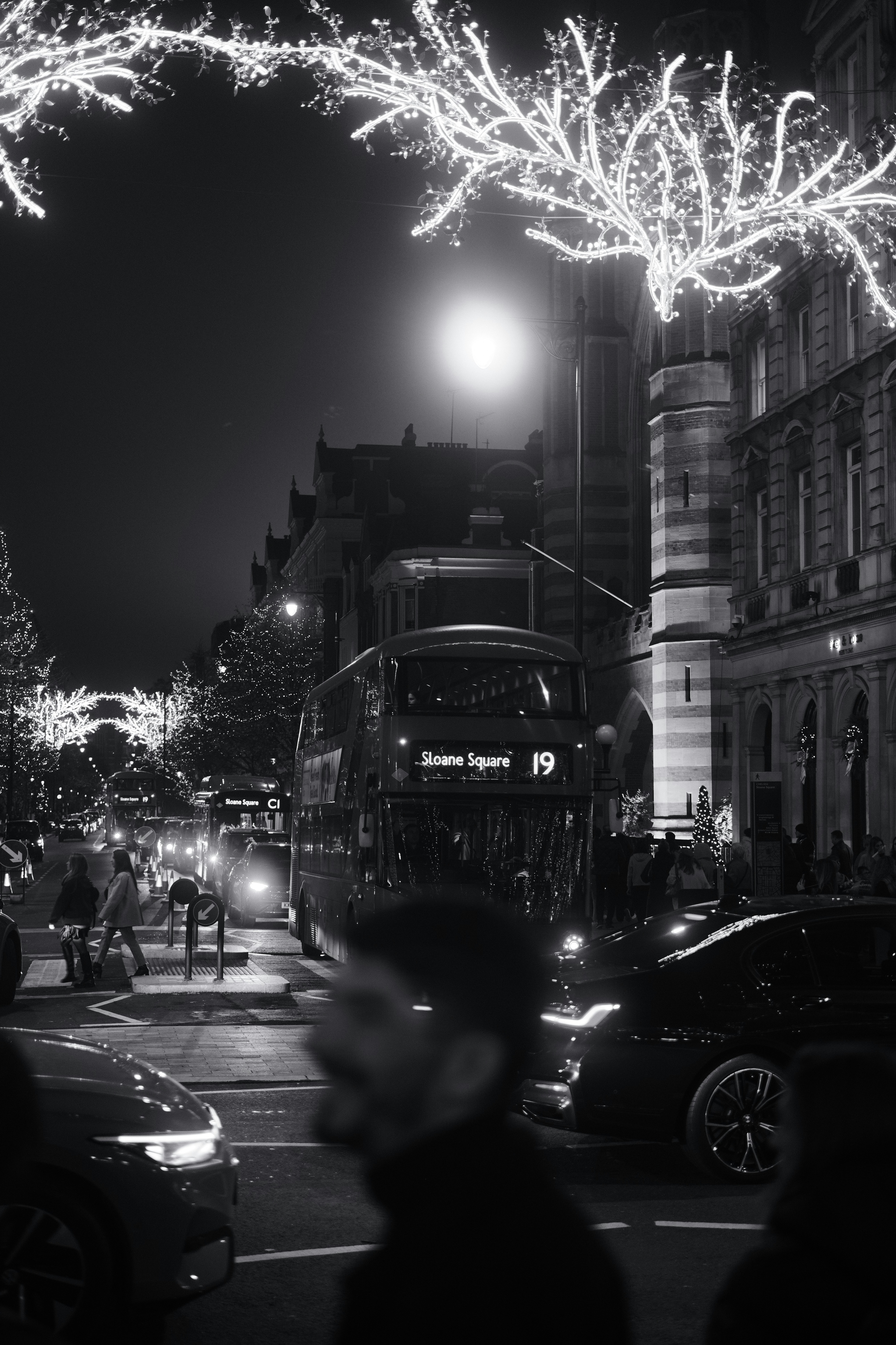Midnight Sloane Square: a glowing double-decker under festive street lights