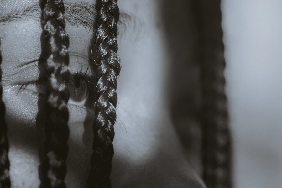 Close-up monochrome portrait with braids falling across part of a face, highlighting one eye in soft focus. The shallow depth of field creates an intimate, moody look.