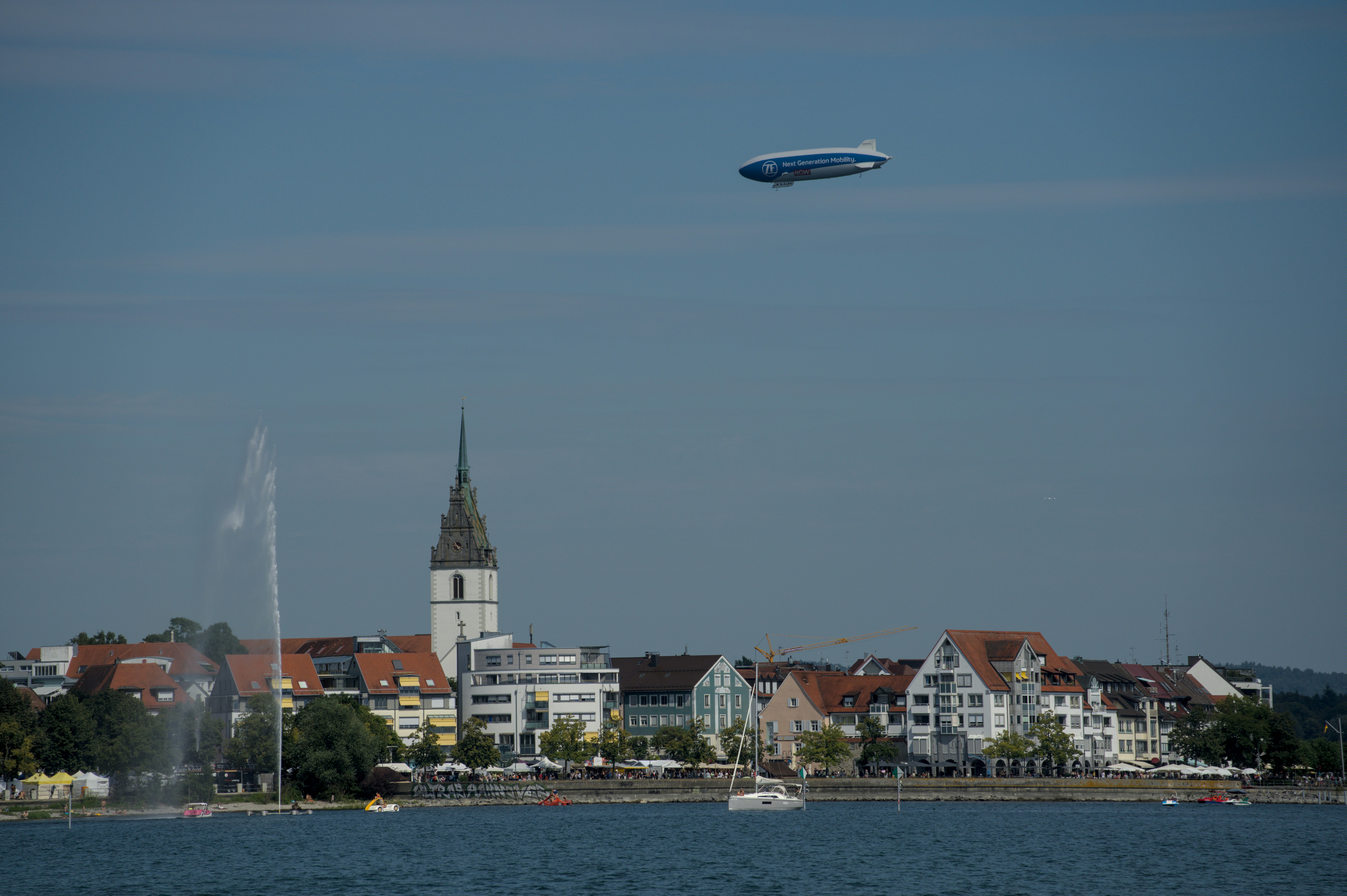 Zeppelin Over the Seaside Town: A Floating Guest Above Red Rooftops and a Tall Spire
