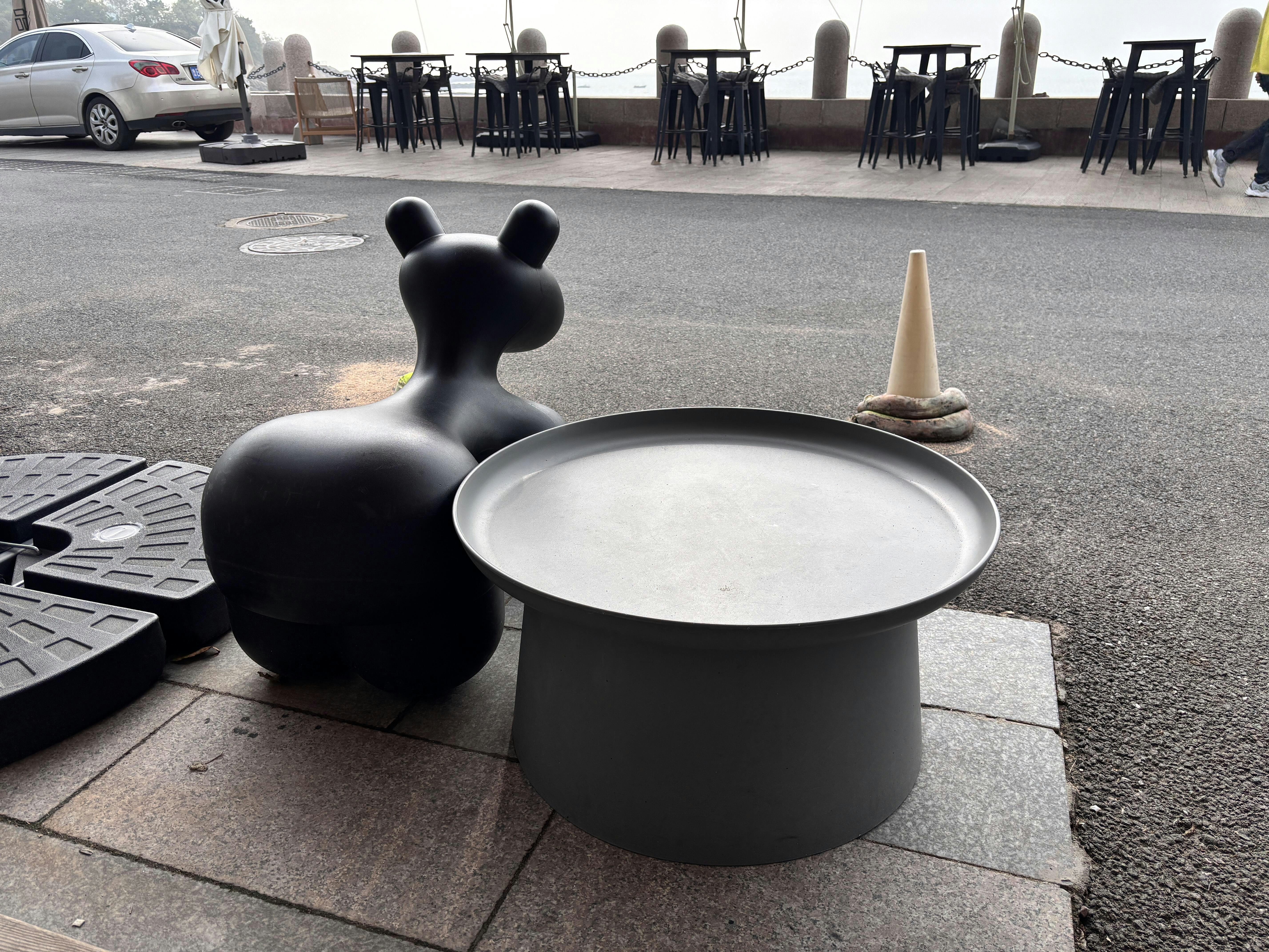 Promenade Sentinel: Matte Black Sculpture Beside a Circular Pedestal on the Waterfront Walk