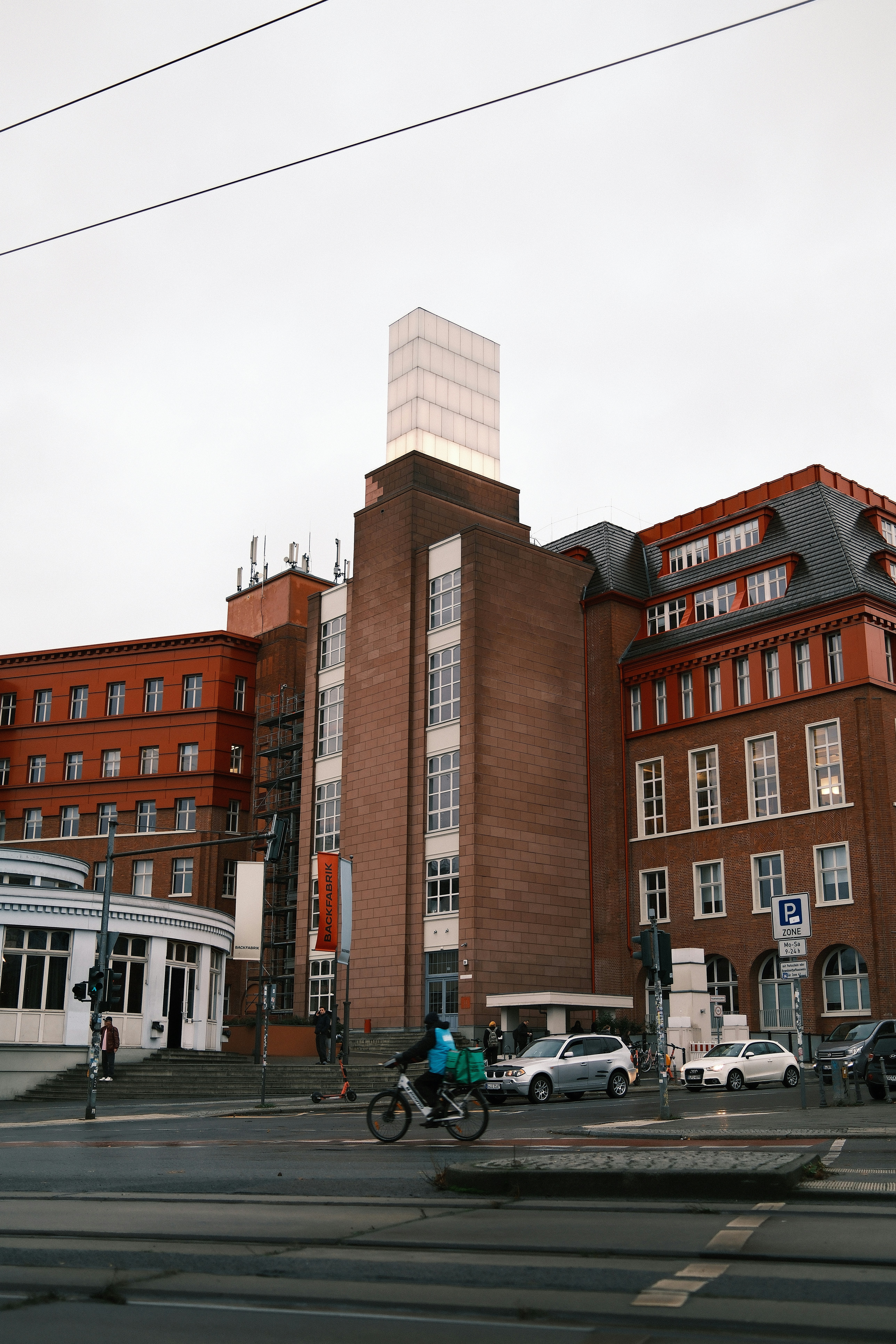A cyclist rides past a large brick building. photo – Free Architecture ...