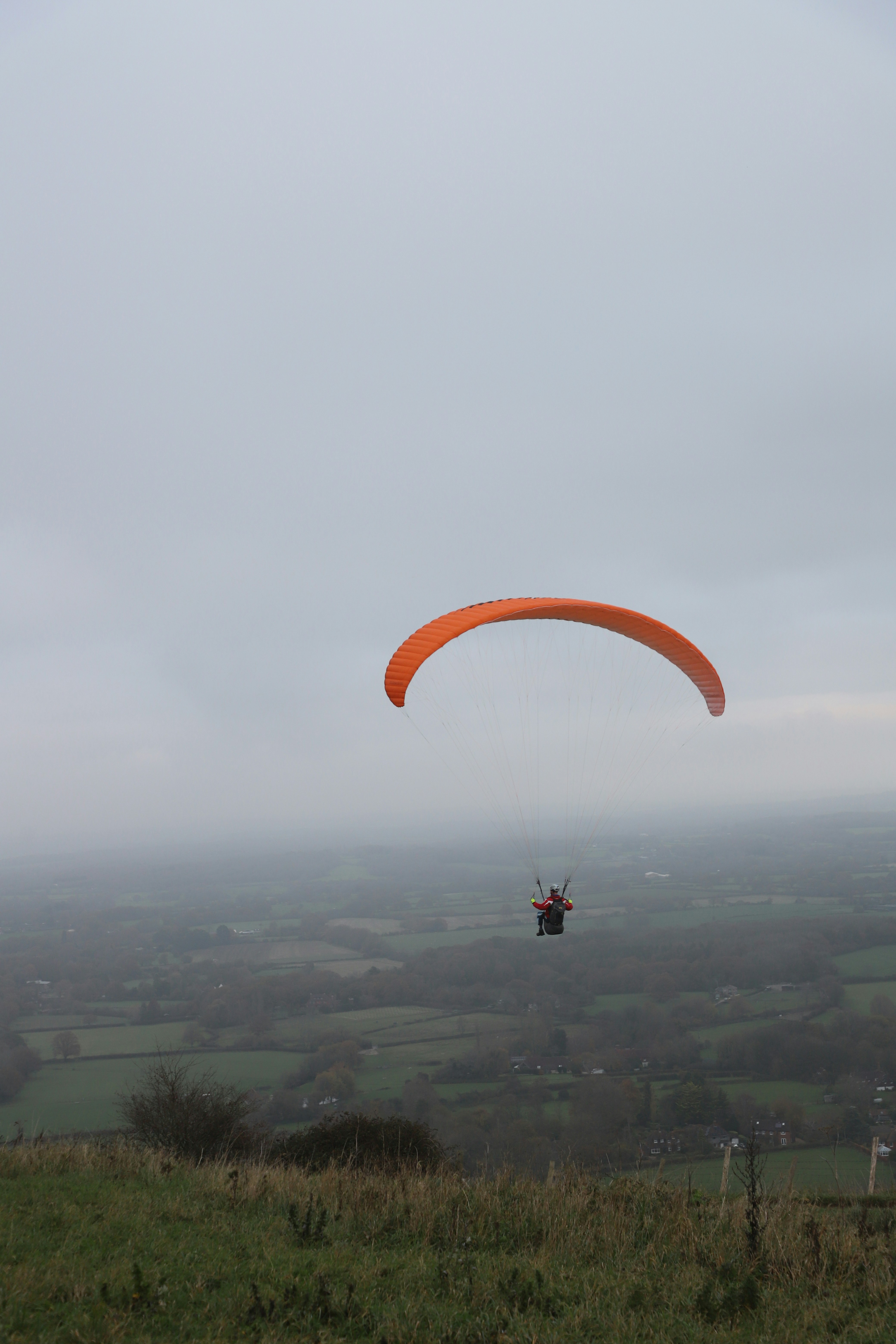Orange Arc Above Patchwork Valleys: A Paraglider’s Quiet Descent