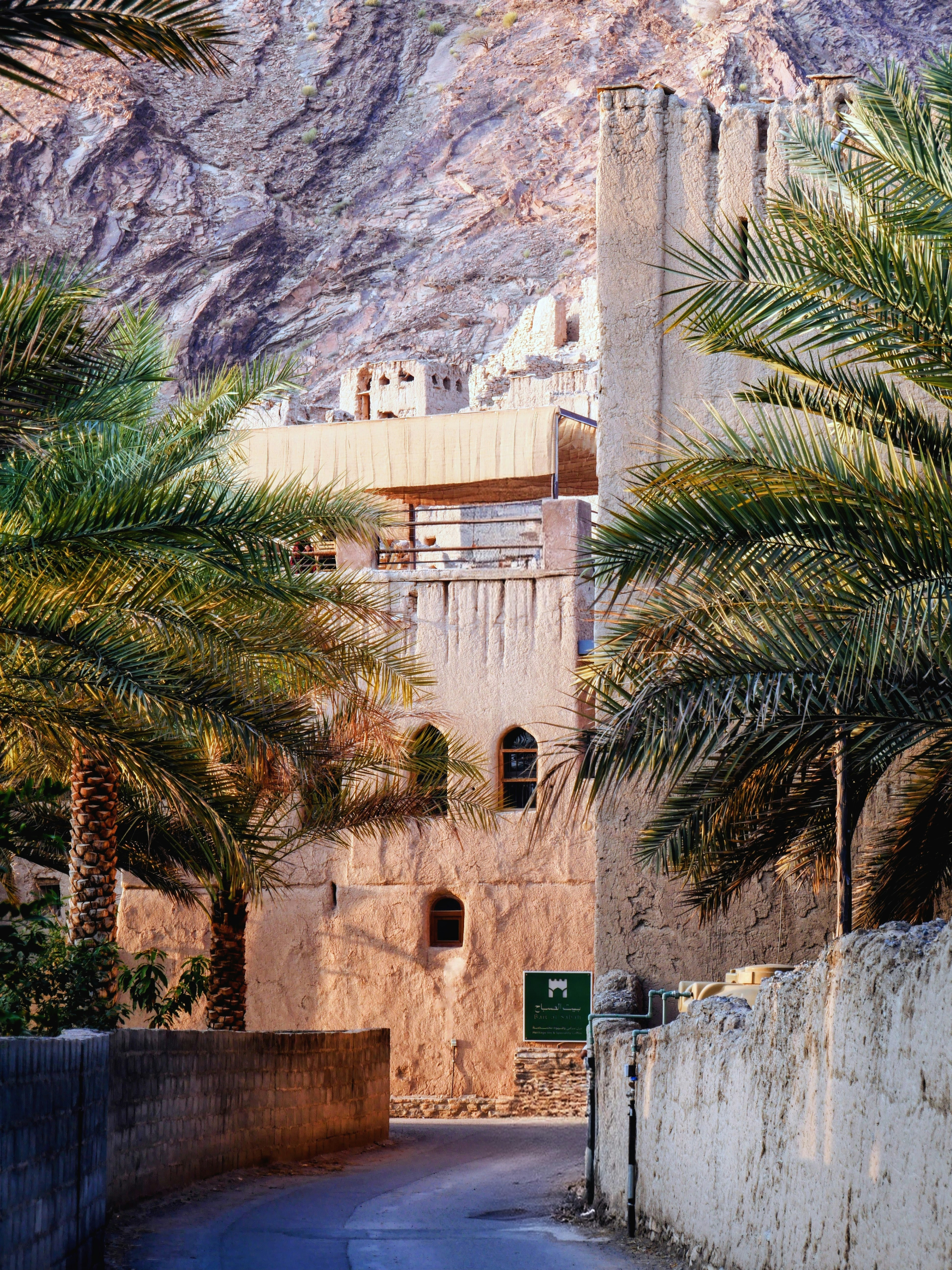 A charming traditional building in Birkat Al Mouz, Oman, featuring rustic stone walls and arched windows that reflect the region’s rich architectural heritage. The image highlights the timeless beauty of Omani craftsmanship, set against the backdrop of a serene desert landscape and lush palm trees.