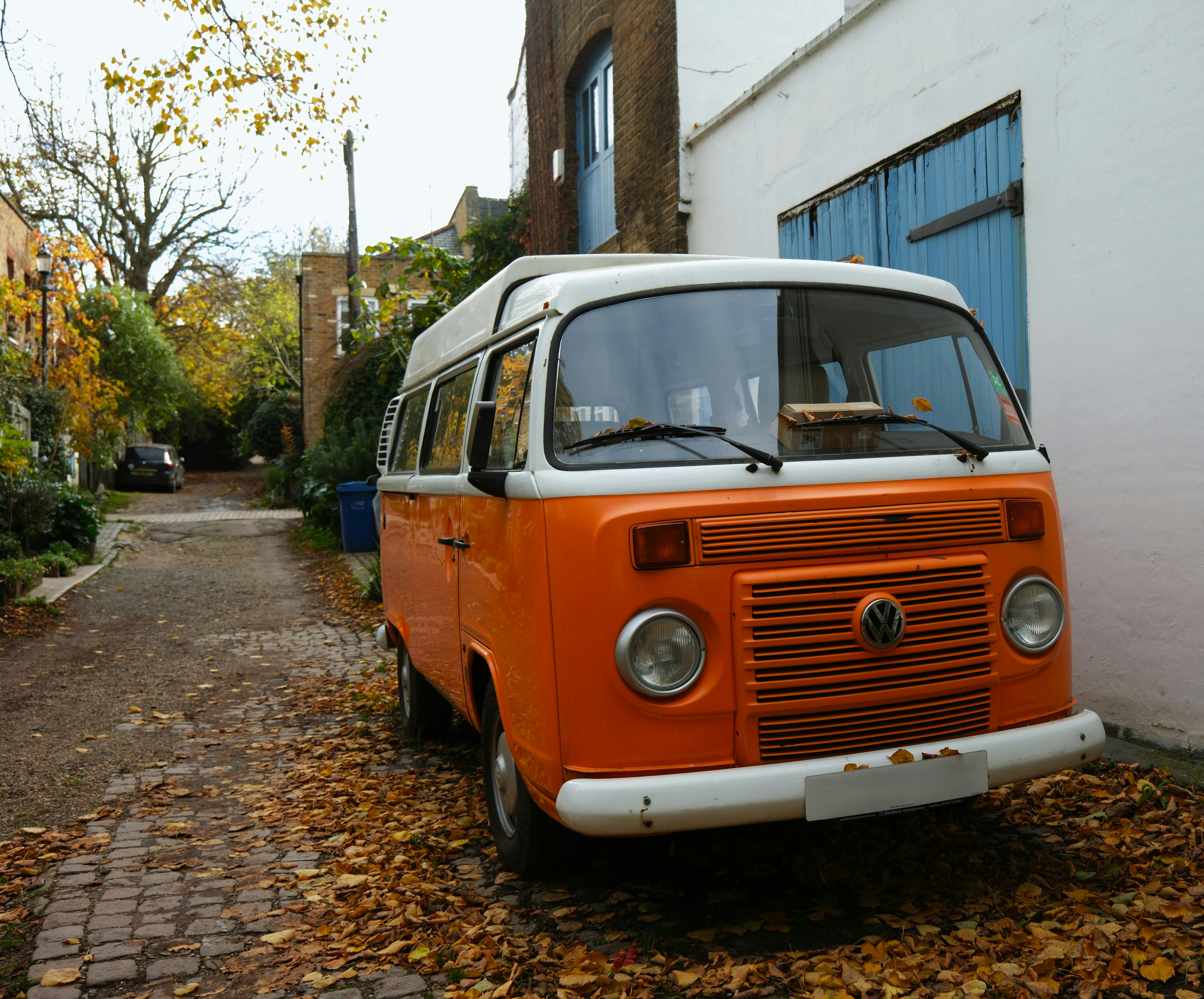 Autumn scene with yellowing leaves falling from the surrounding trees. A classic Volkswagen Transporter in a beautiful white & orange livery is parked in a small road in south London. I have blurred the number plate to protect the owner's privacy.