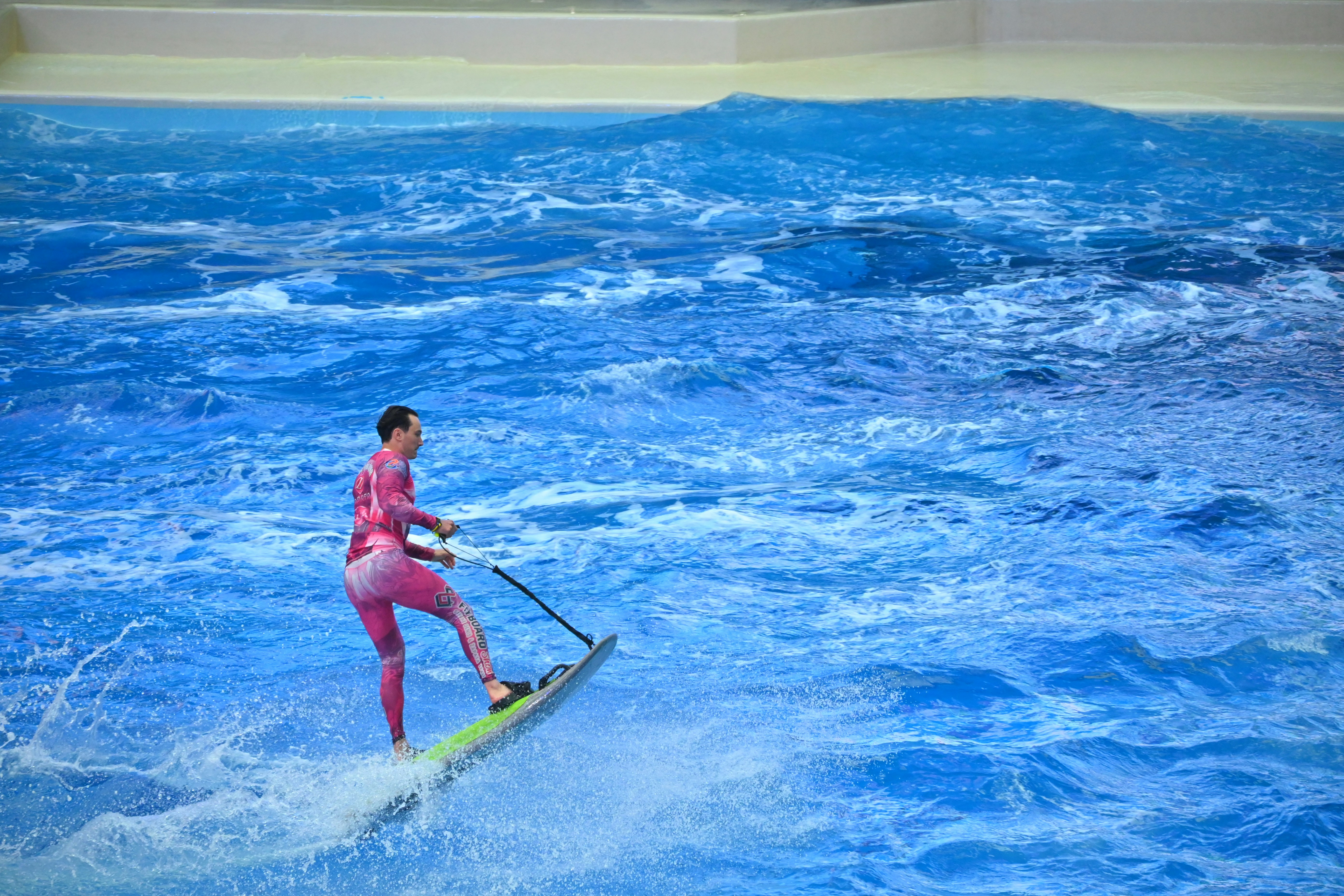 Pink-Suited Surfer Carves a Wake Across an Electric Blue Artificial Wave