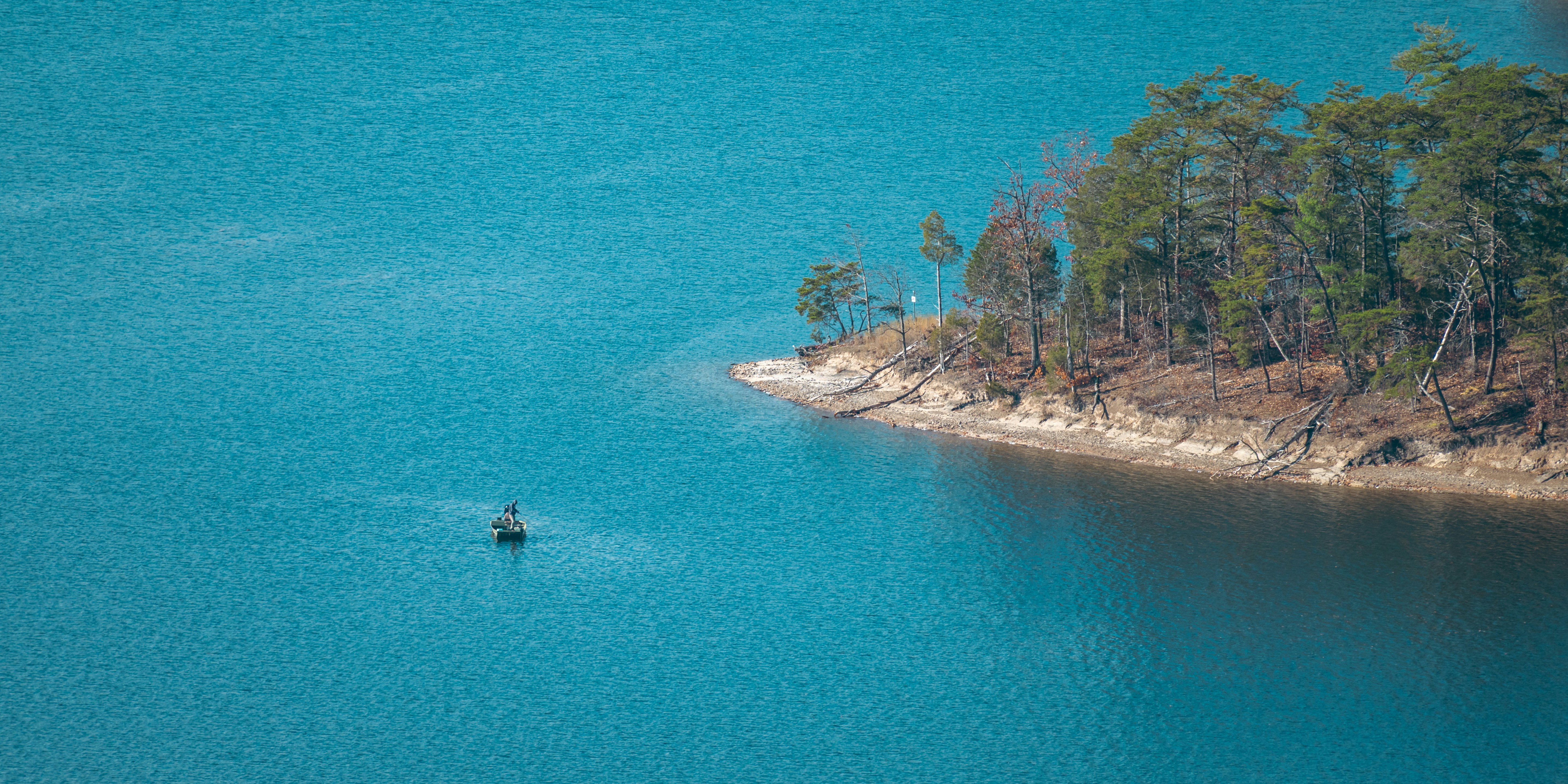 Lone Boat Drifting Across Turquoise Waters by a Pine-Covered Peninsula