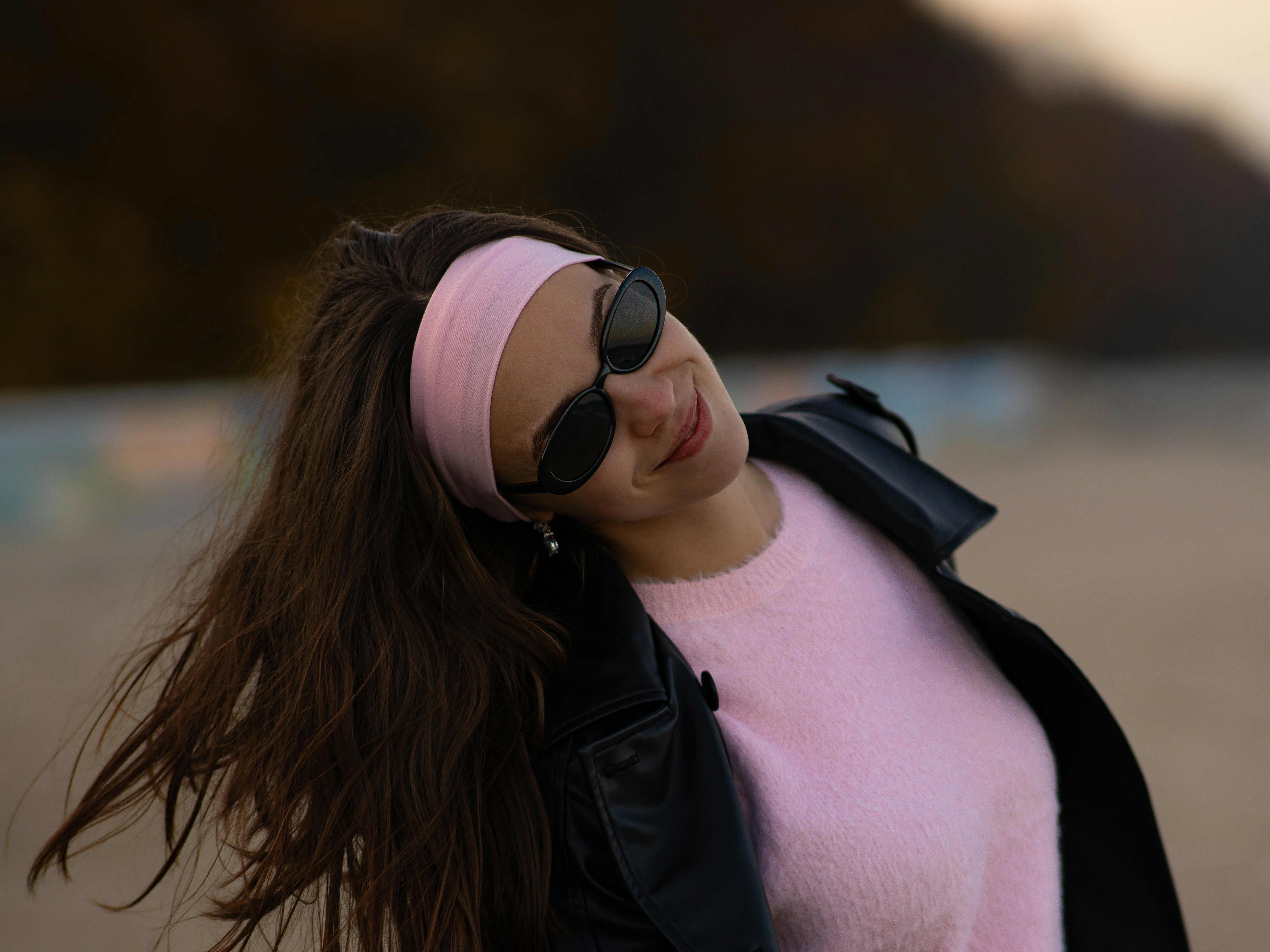 Sun-kissed beach portrait: pink knit, leather jacket, and wind-swept confidence