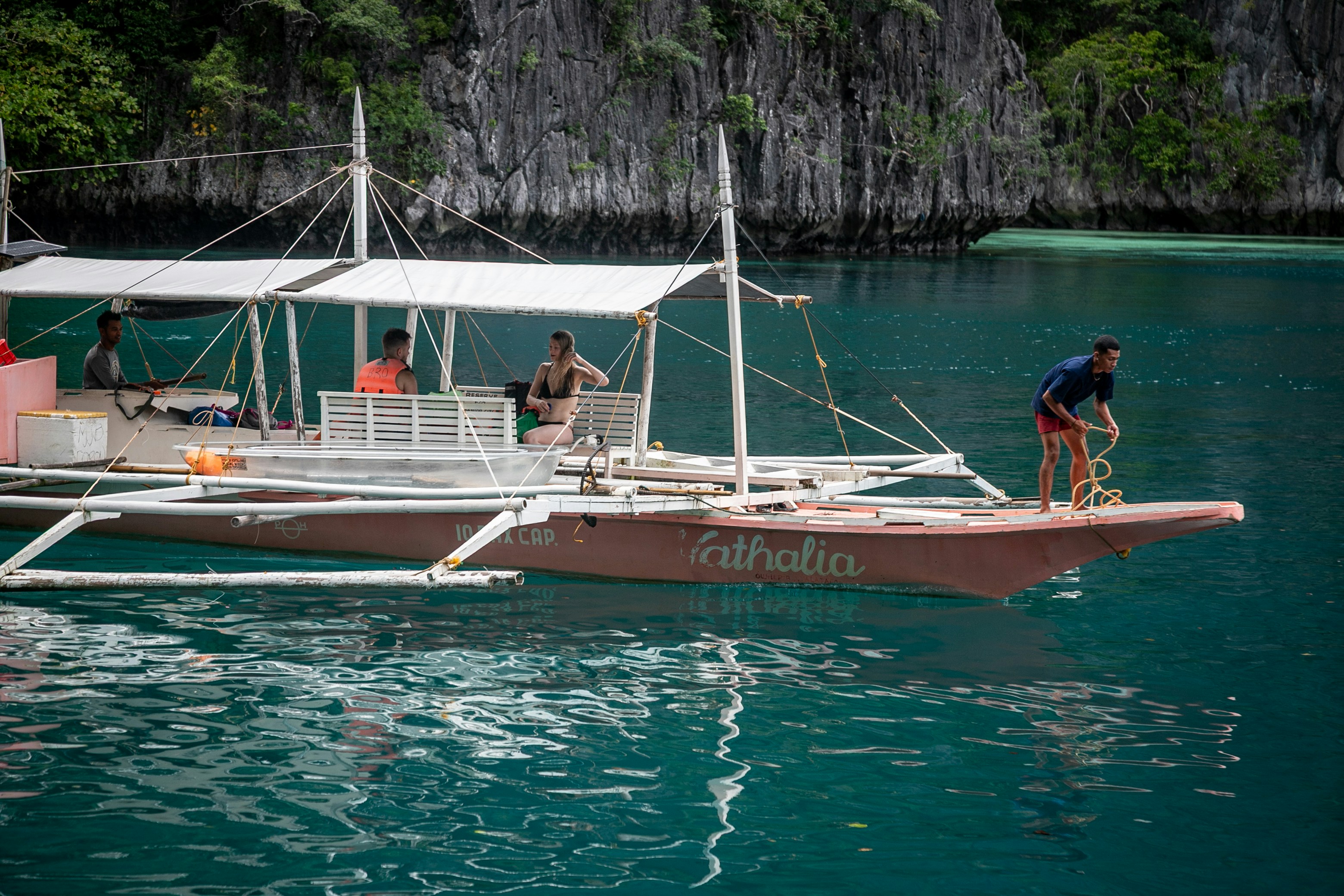 Reel and Rise: Crewman Handling Lines on a Pink-Hulled Boat in Turquoise Waters