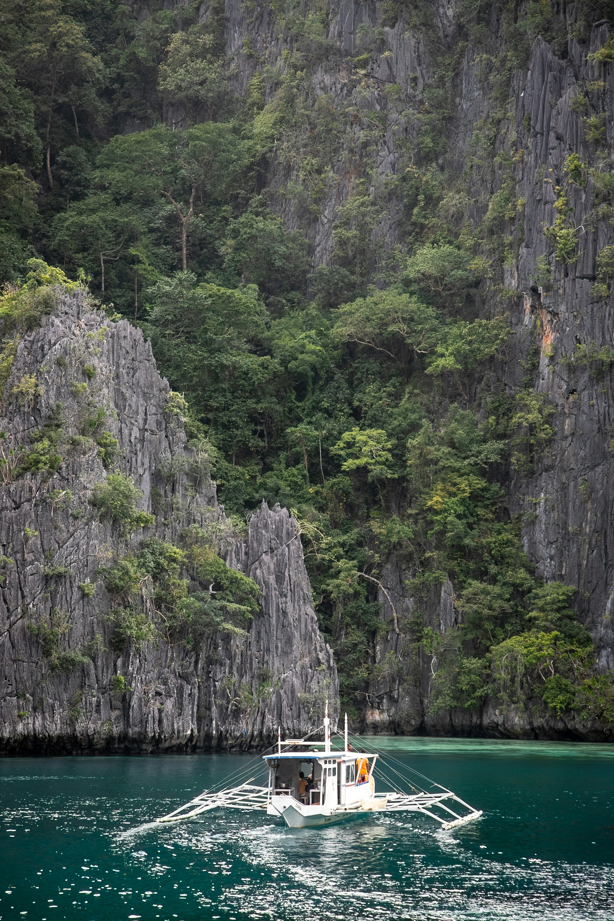 Emerald Inlet Outrigger: A lone boat against turquoise water and towering limestone cliffs