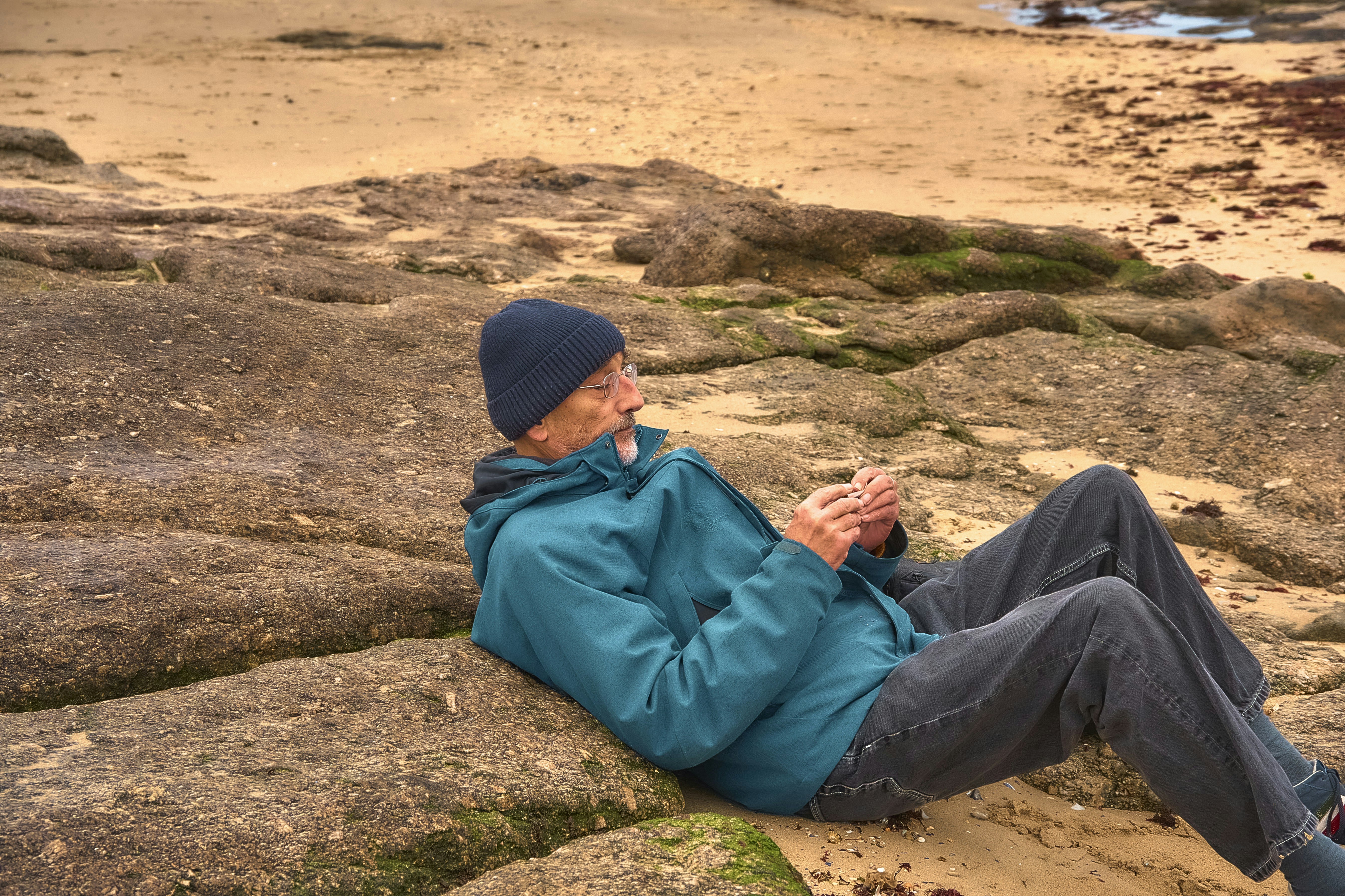 Coastal Repose: a man in teal lounges on mossy rocks by the shore