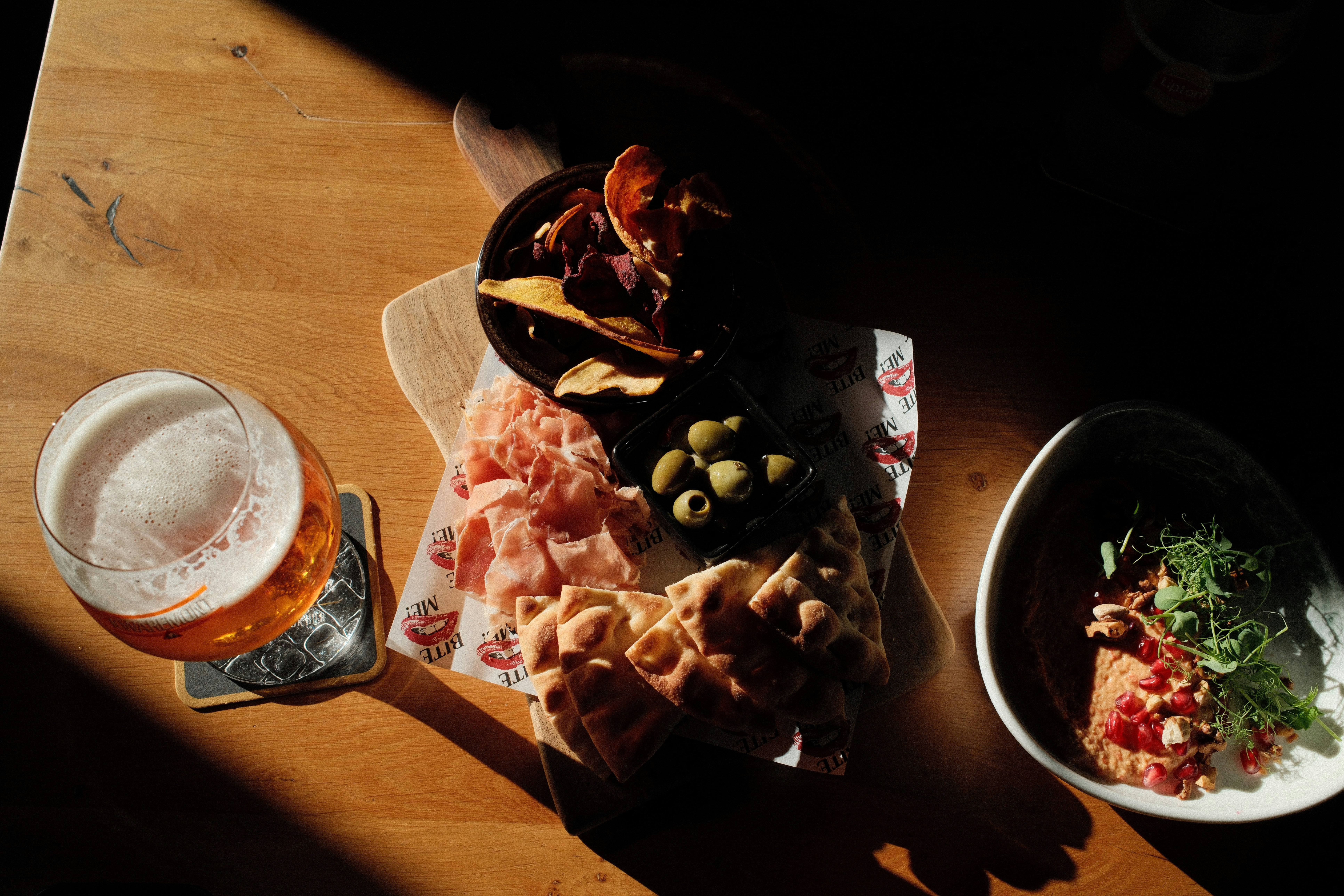 Sunlit Tapas Board: Olives, Pita, and Amber Ale on a Wooden Table