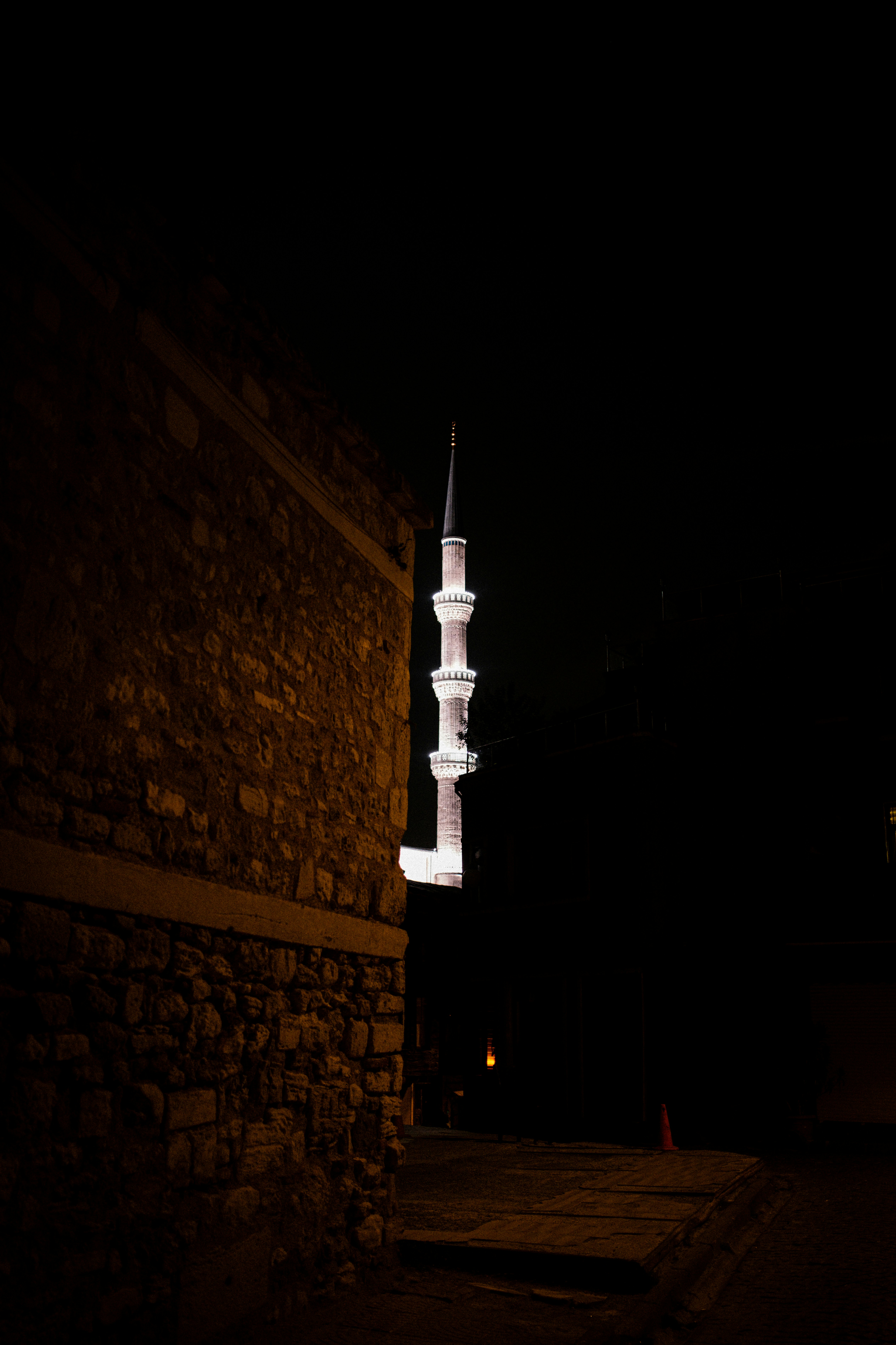 Luminous Minaret Piercing the Night from a Shadowed Alley