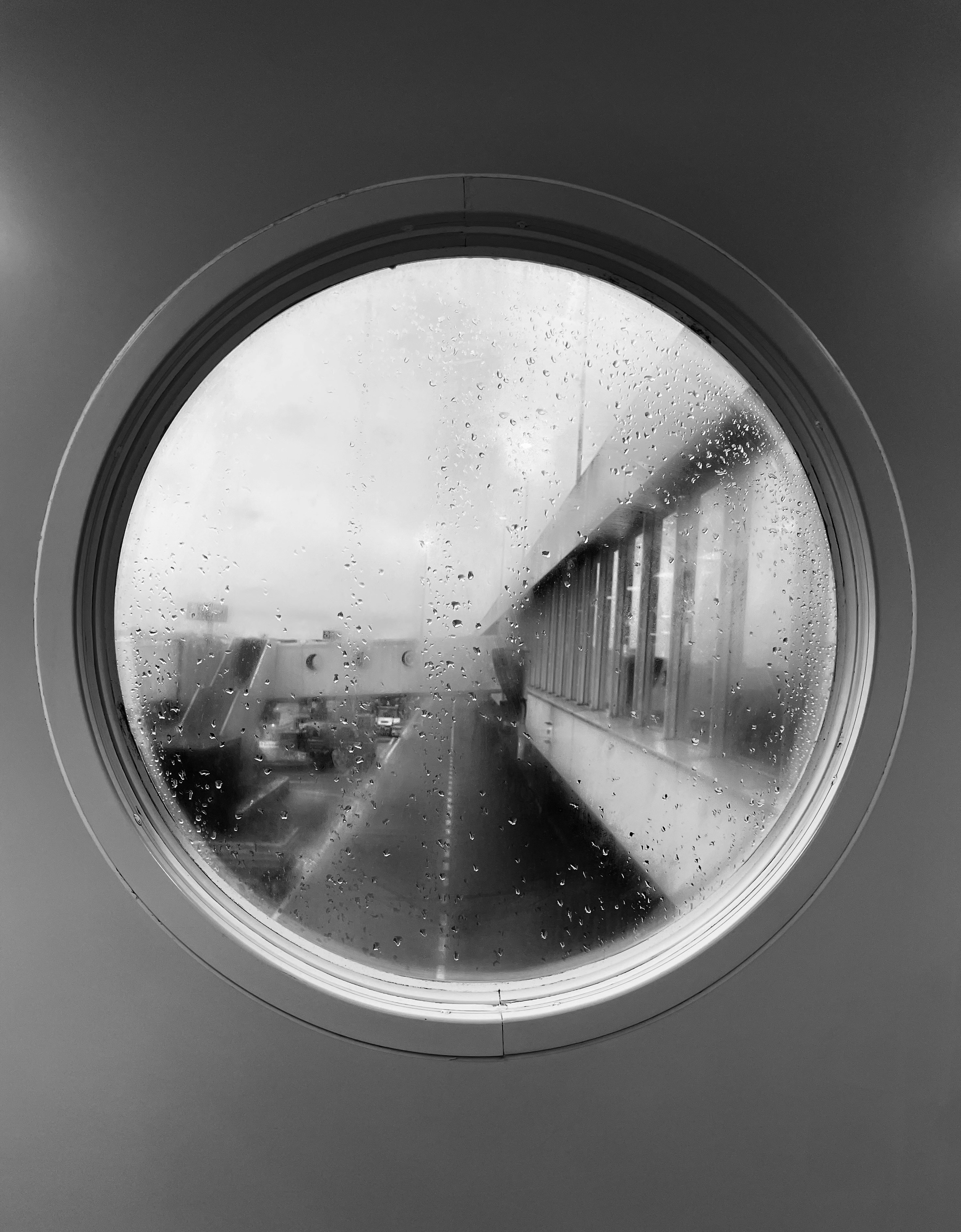 Rain-Streaked Porthole: A Monochrome Corridor Beyond the Glass