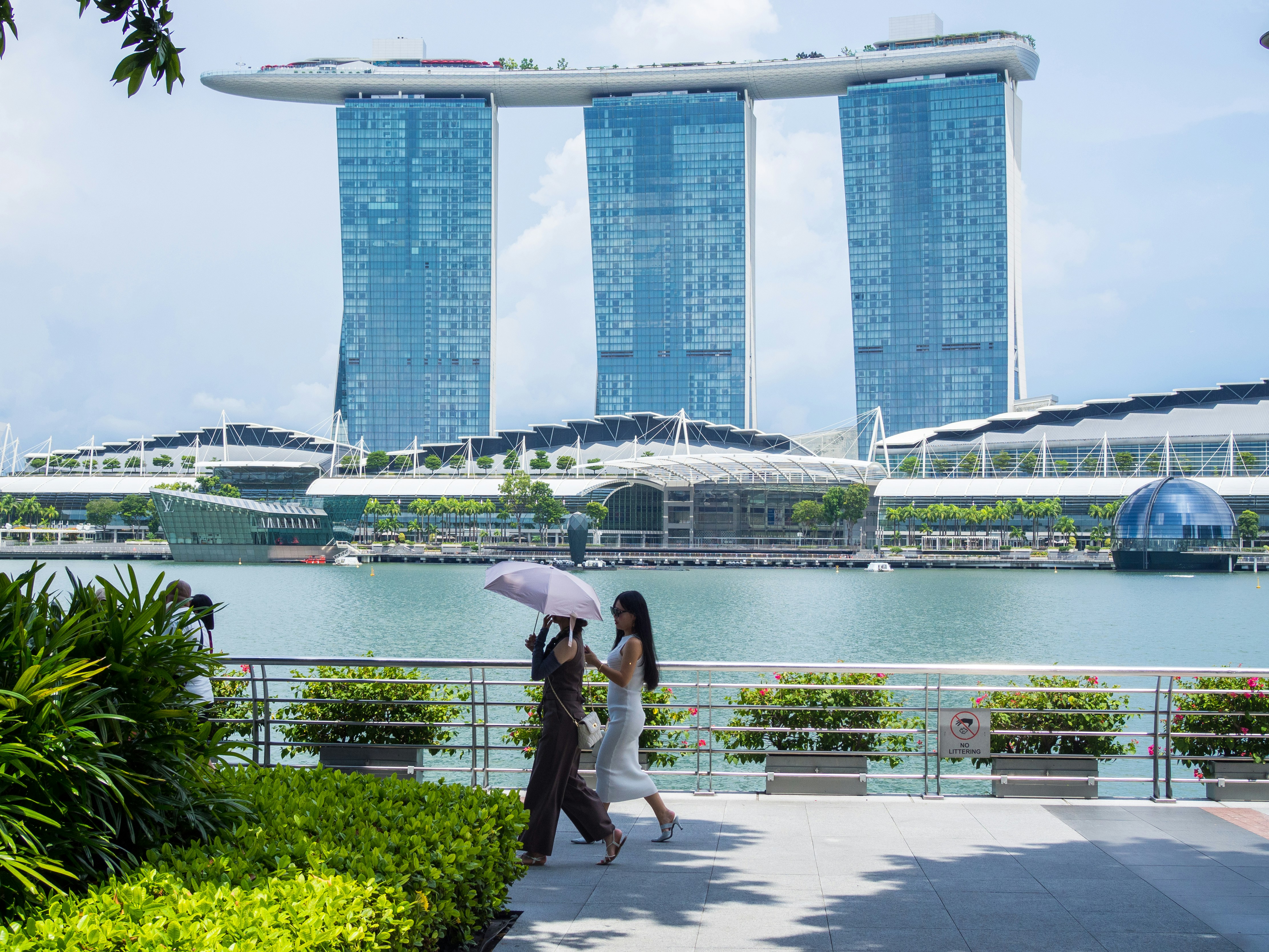 Two women walk by a waterfront with skyscrapers behind them photo ...
