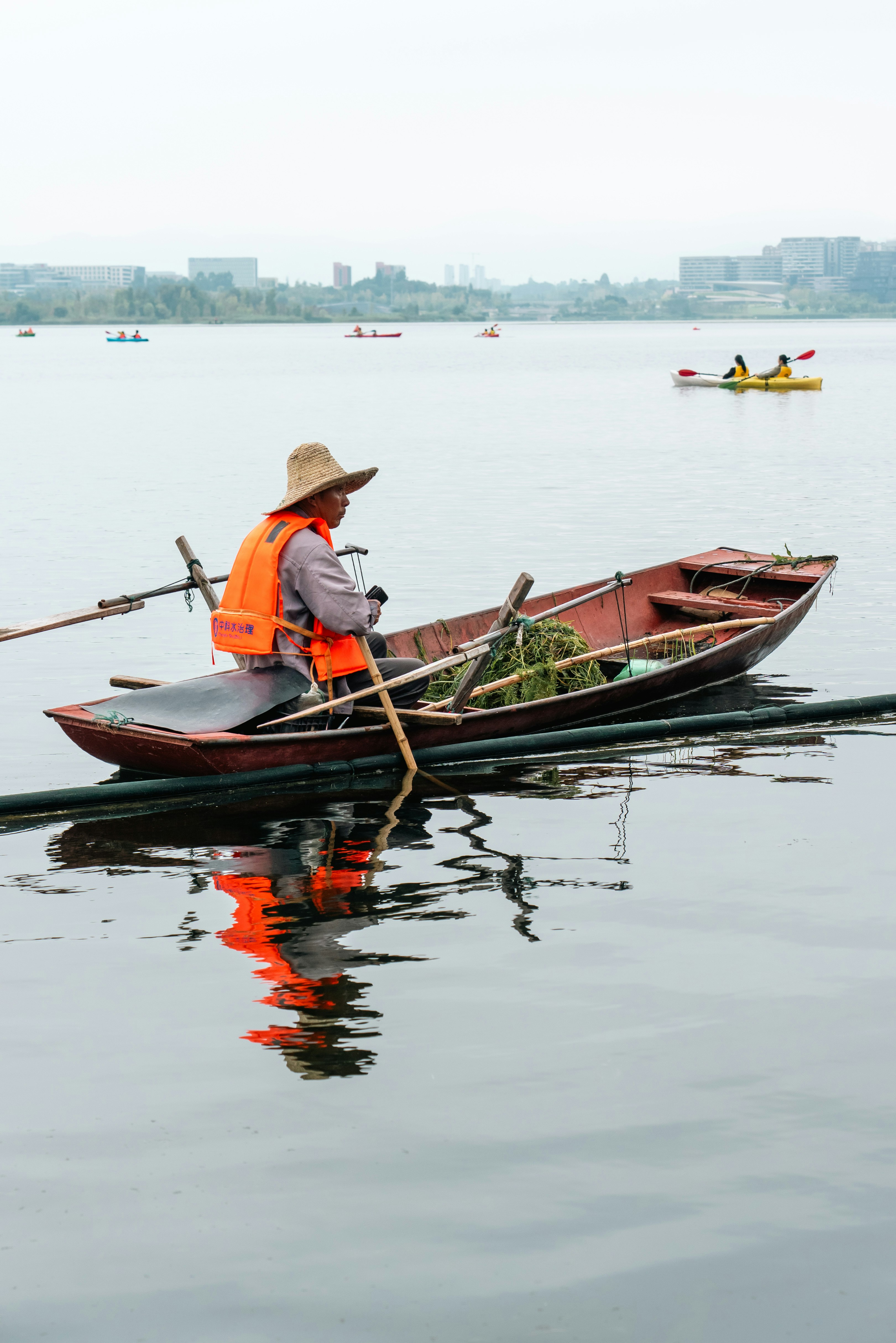 Orange-vested Helmsman in a Red Rowboat on a Calm Urban Lake