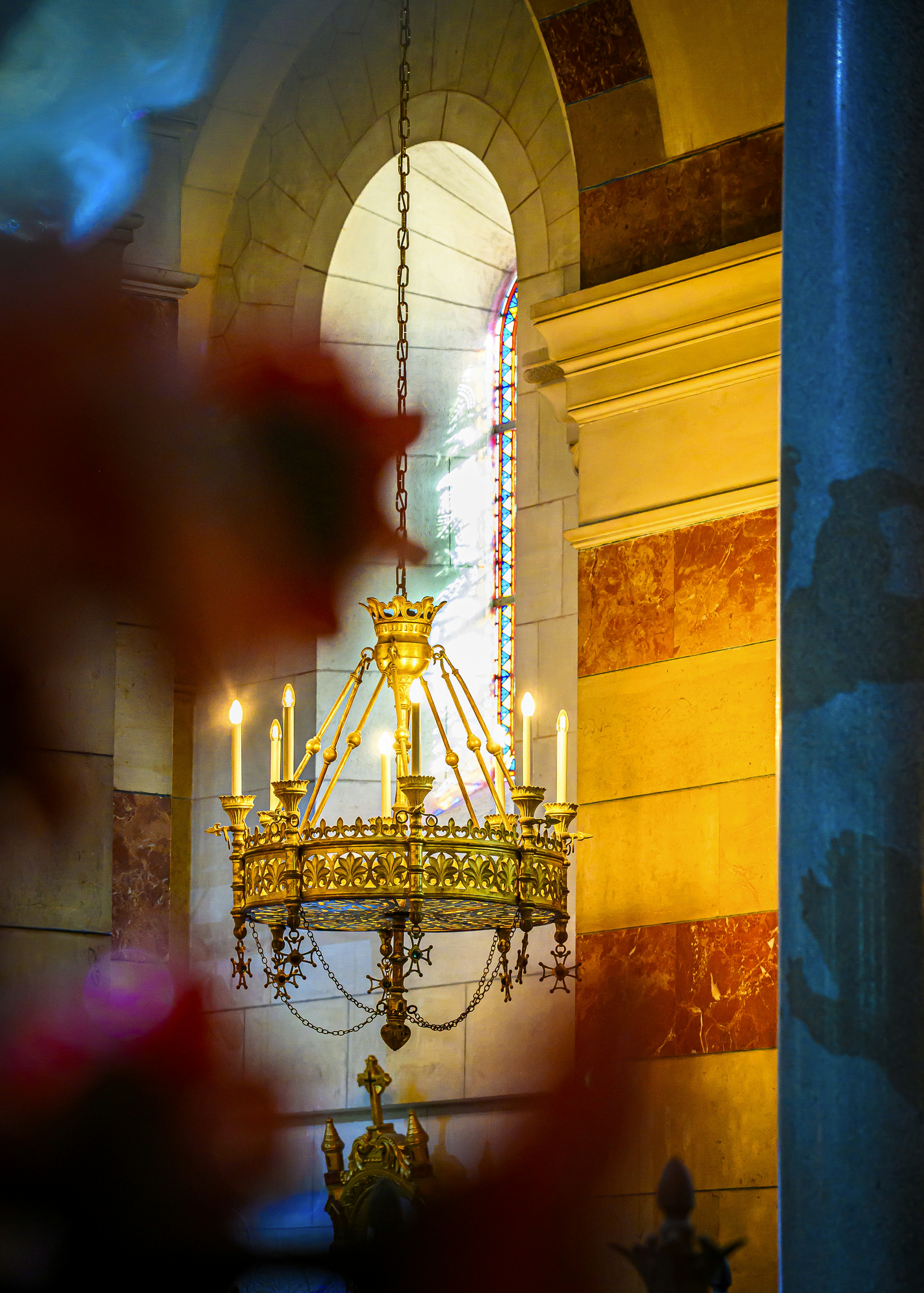 Golden chandelier in a sunlit chapel framed by colored stone walls