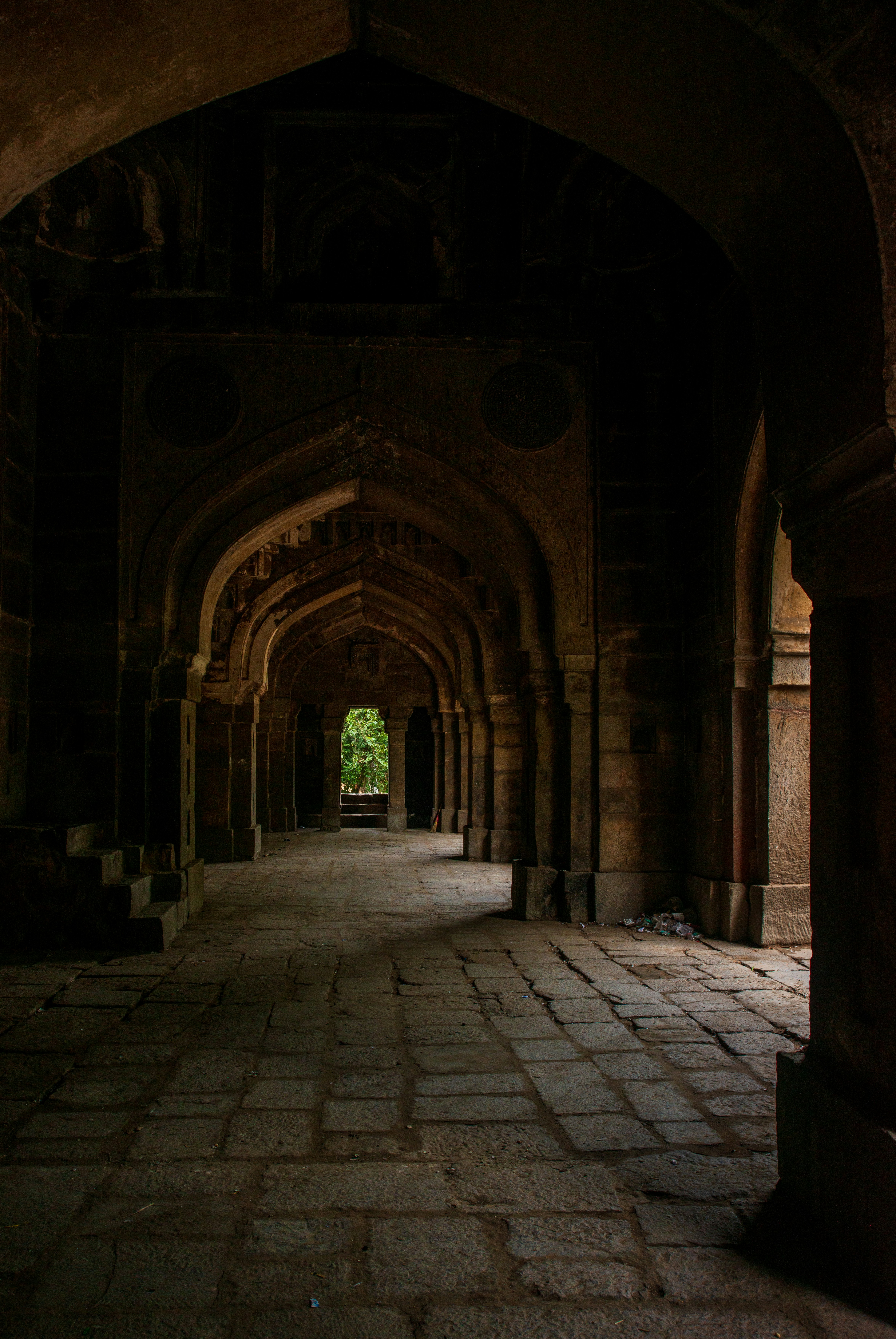 The interior corridor of Masjid Moth is built entirely of stone and lined with repeating arches through which warm light filters in. This mosque dates to the Lodhi era and was commissioned in the early 1500s. According to historical accounts, Sultan Sikandar Lodi granted a bag of moth lentils to his prime minister, Wazir Miya Bhoiya, who used its sale to fund the construction of the mosque. Over time the structure became known as Masjid Moth in reference to that origin. The building reflects characteristic Lodhi period work with robust stonework, pointed arches, and sequences of vaulted bays.
