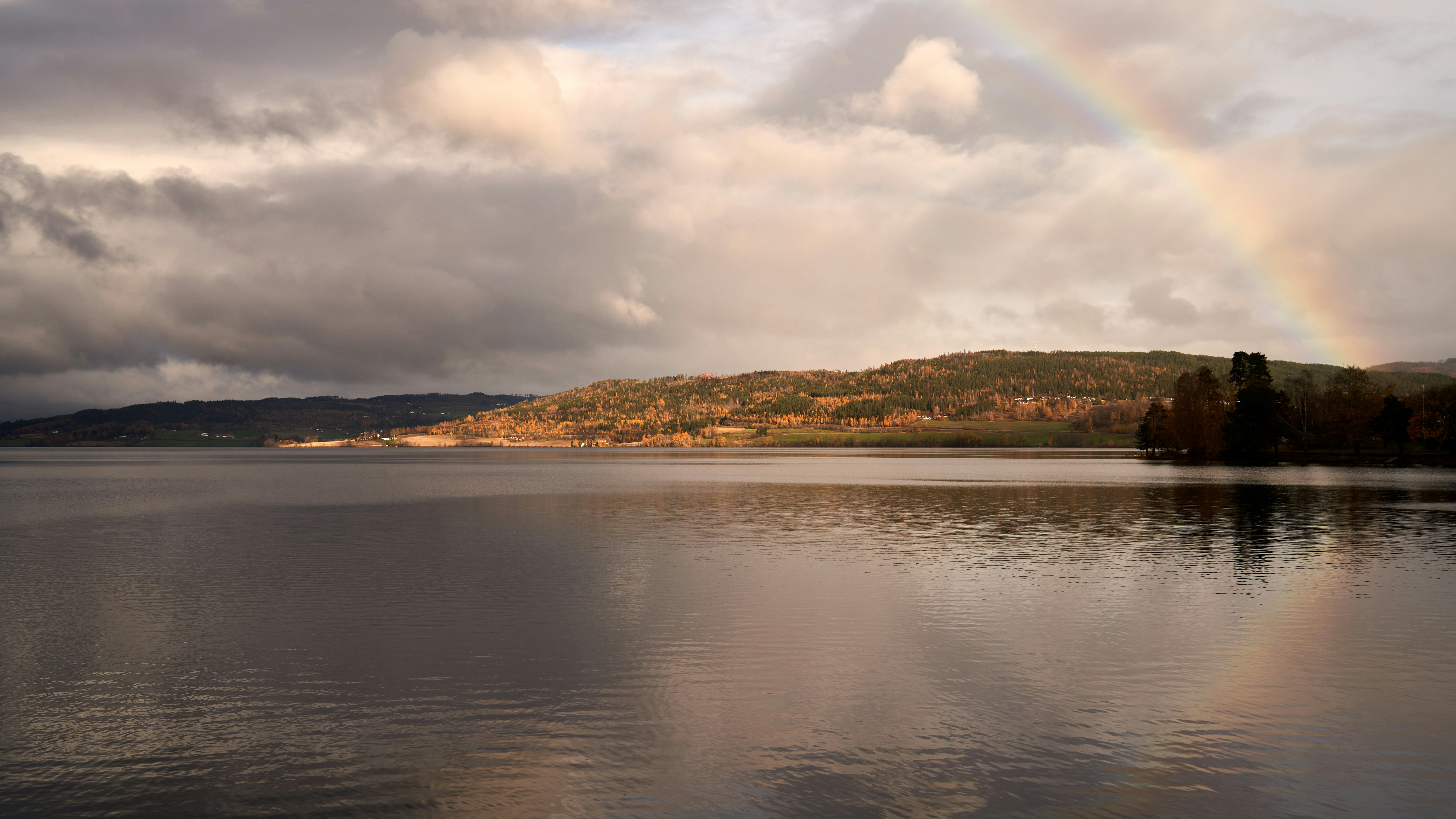 Rainbow Arc Over a Glassy Lake, Beneath Cloud-Washed Hills