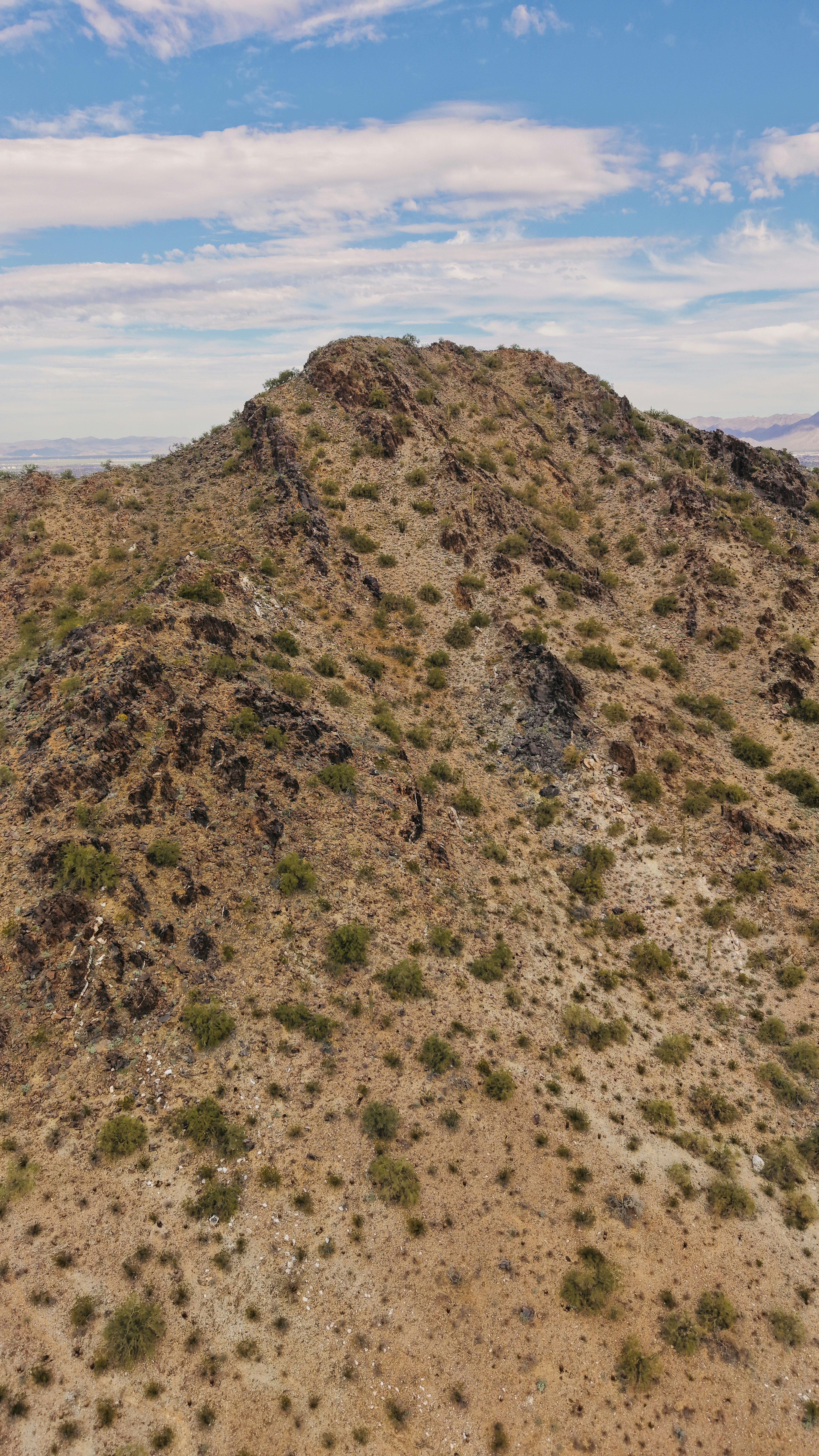 Rocky desert mountain with sparse green vegetation under blue sky.