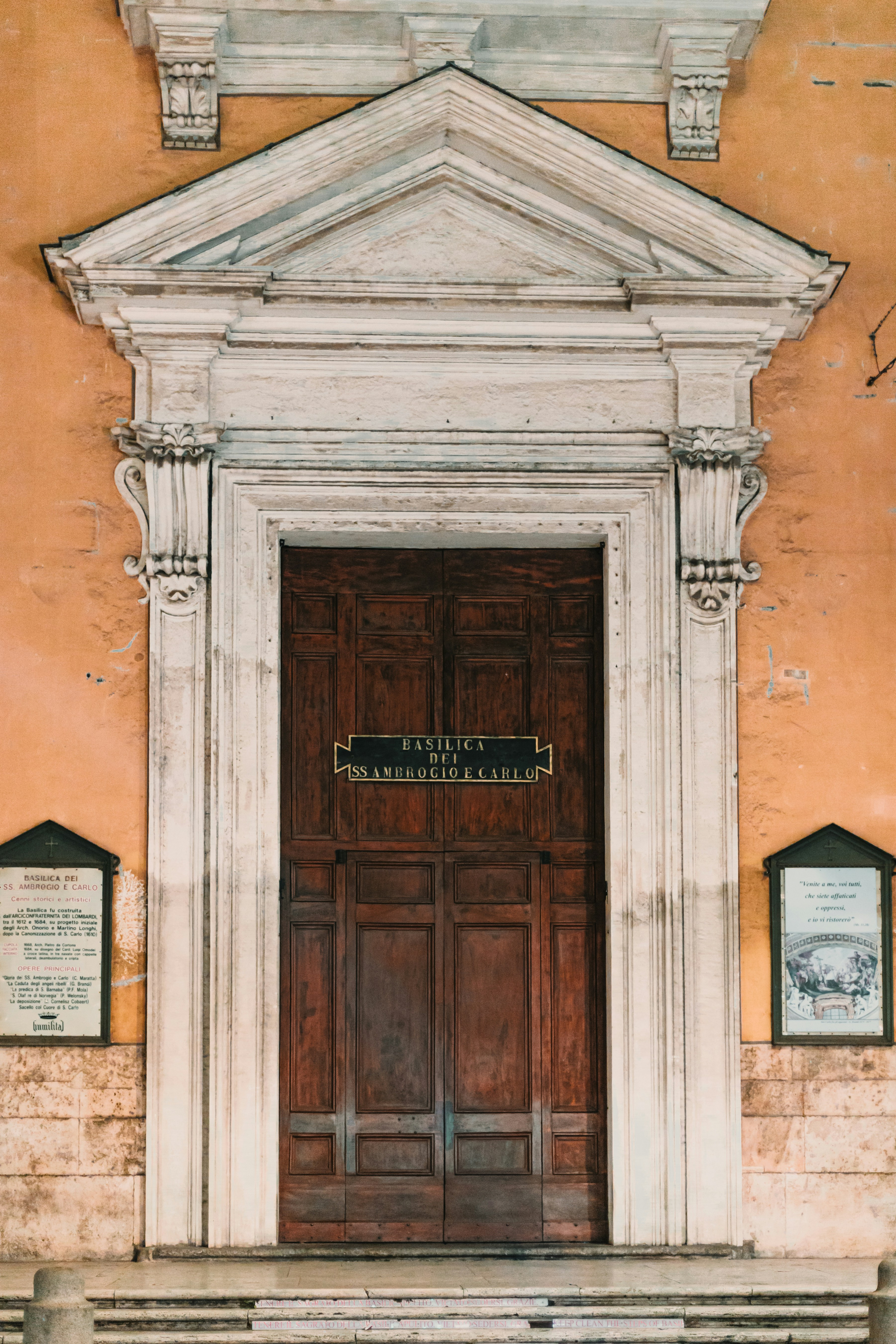 Basilica wooden entrance door with white stone trim and signage on an orange stucco wall.