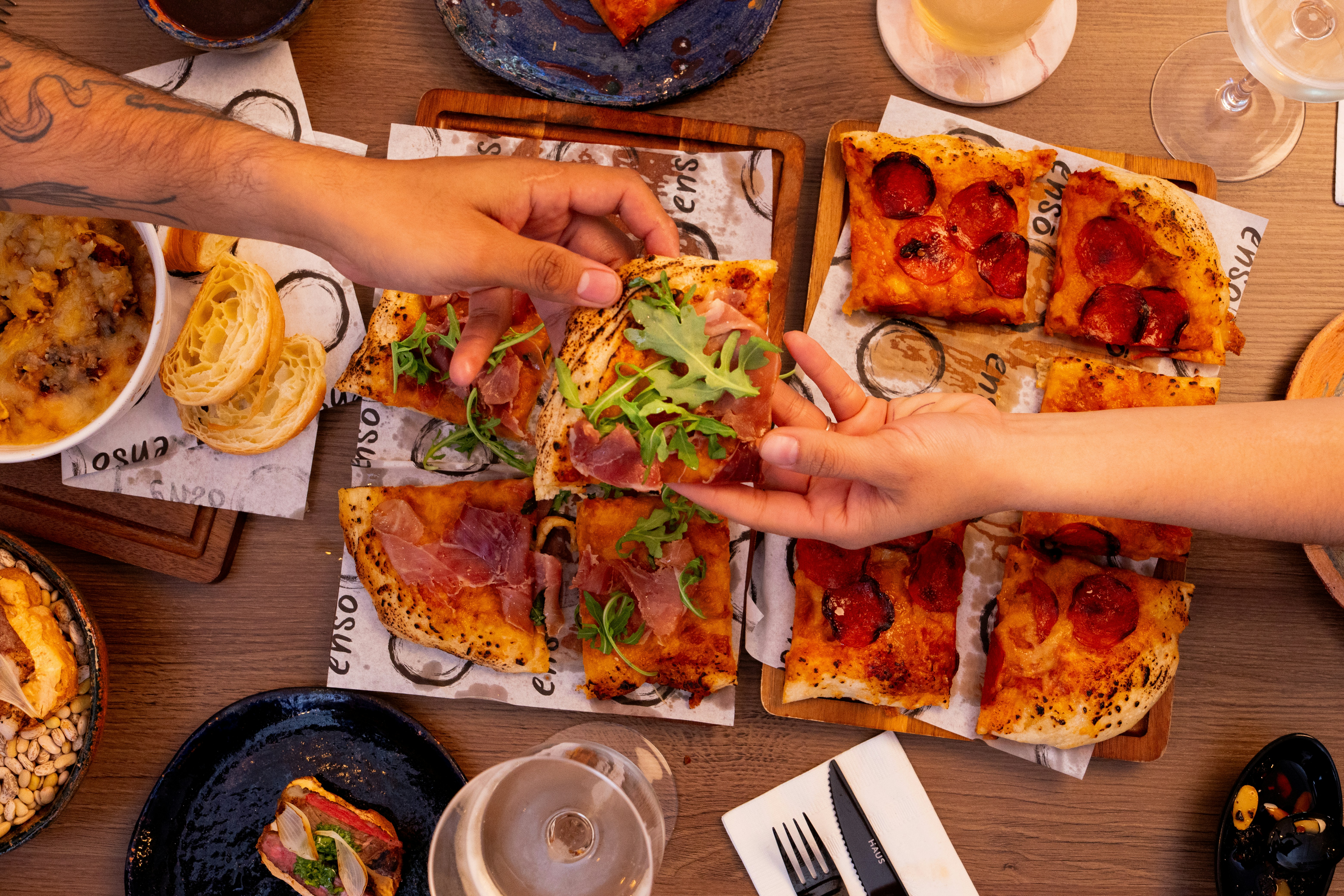 Hands reaching for slices of pizza and food