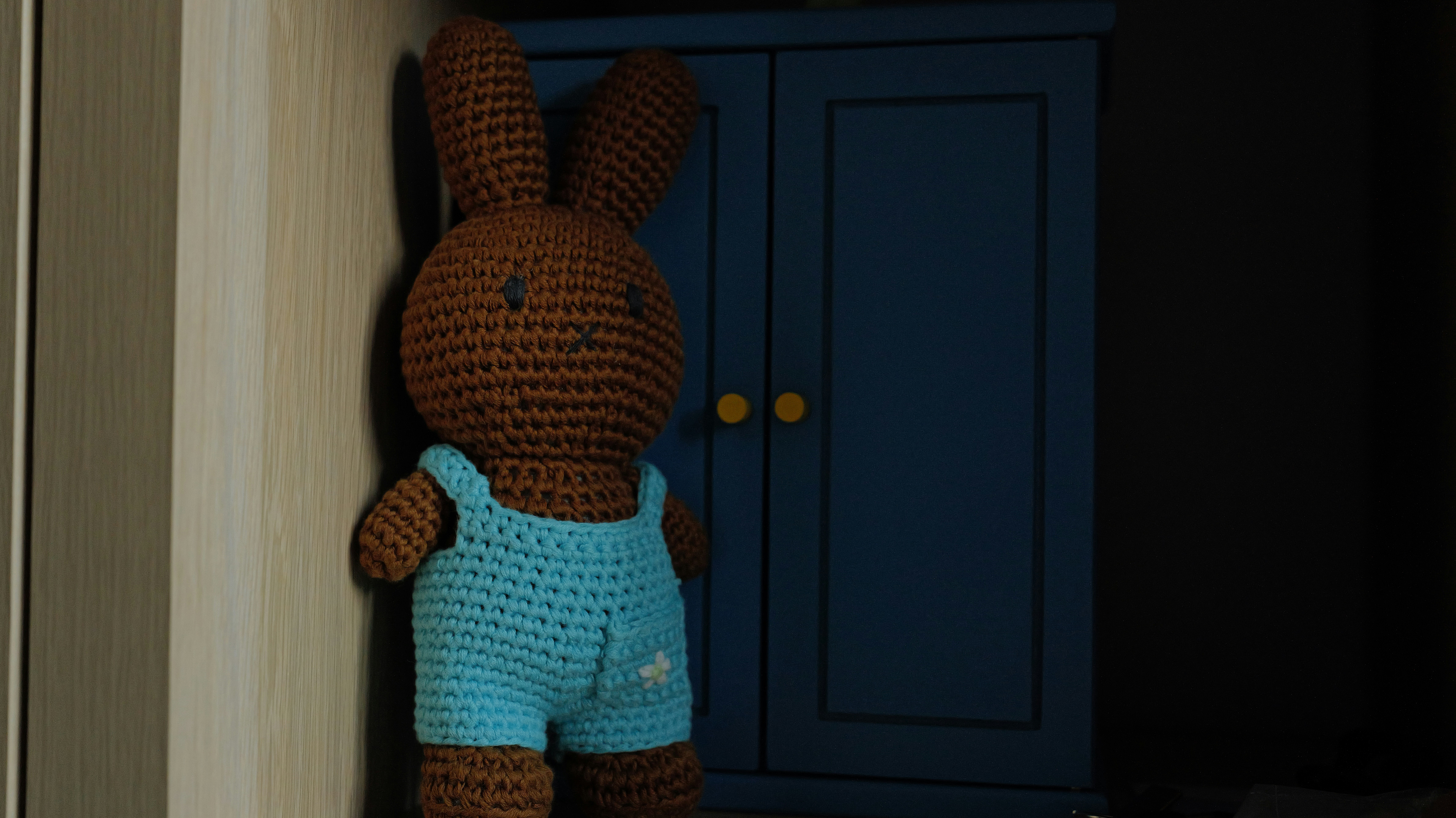 Crocheted Bunny in a Shadowed Corner Beside a Deep Blue Cabinet