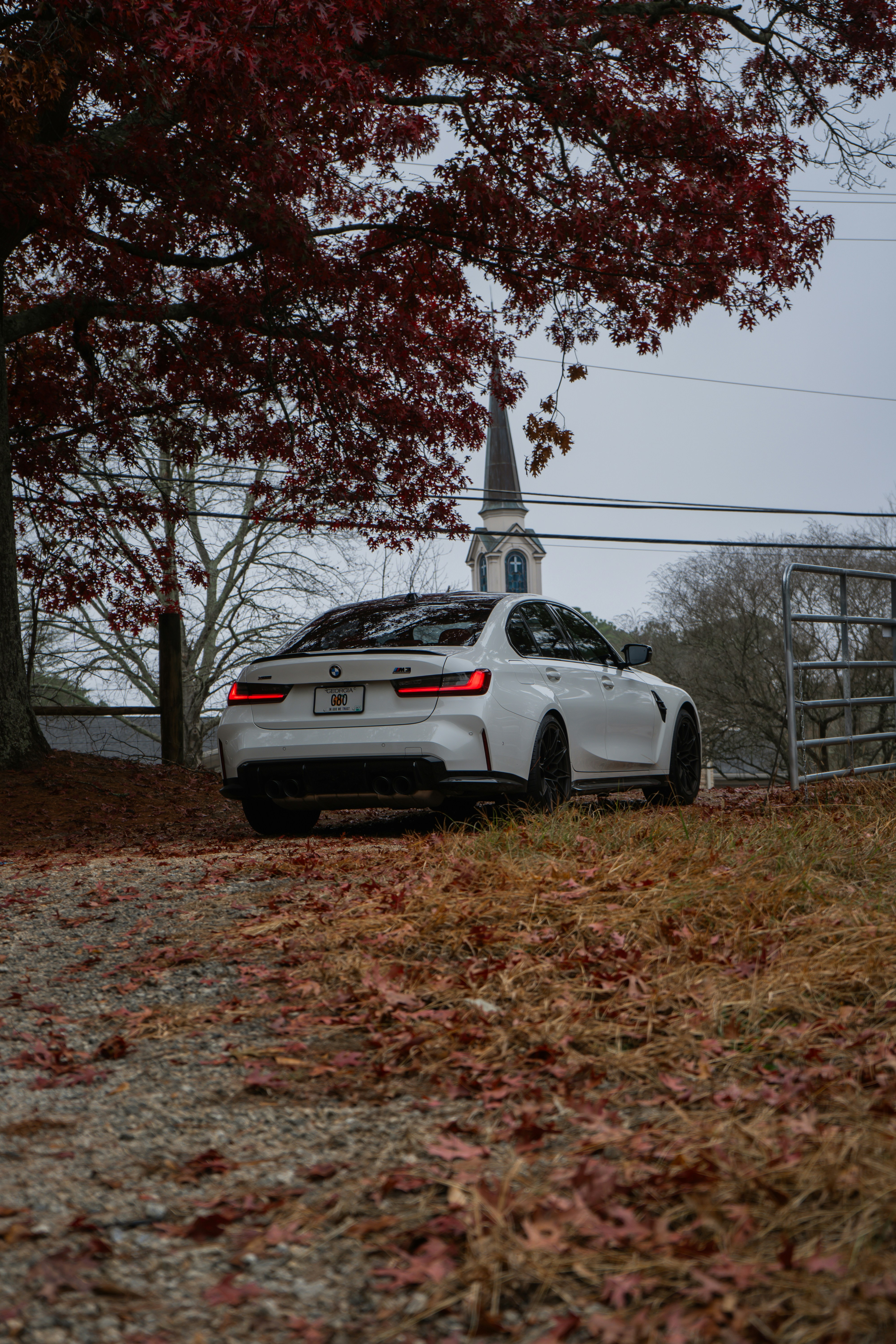 Crimson Canopy Over a White BMW: Autumn Drive by a Quiet Church