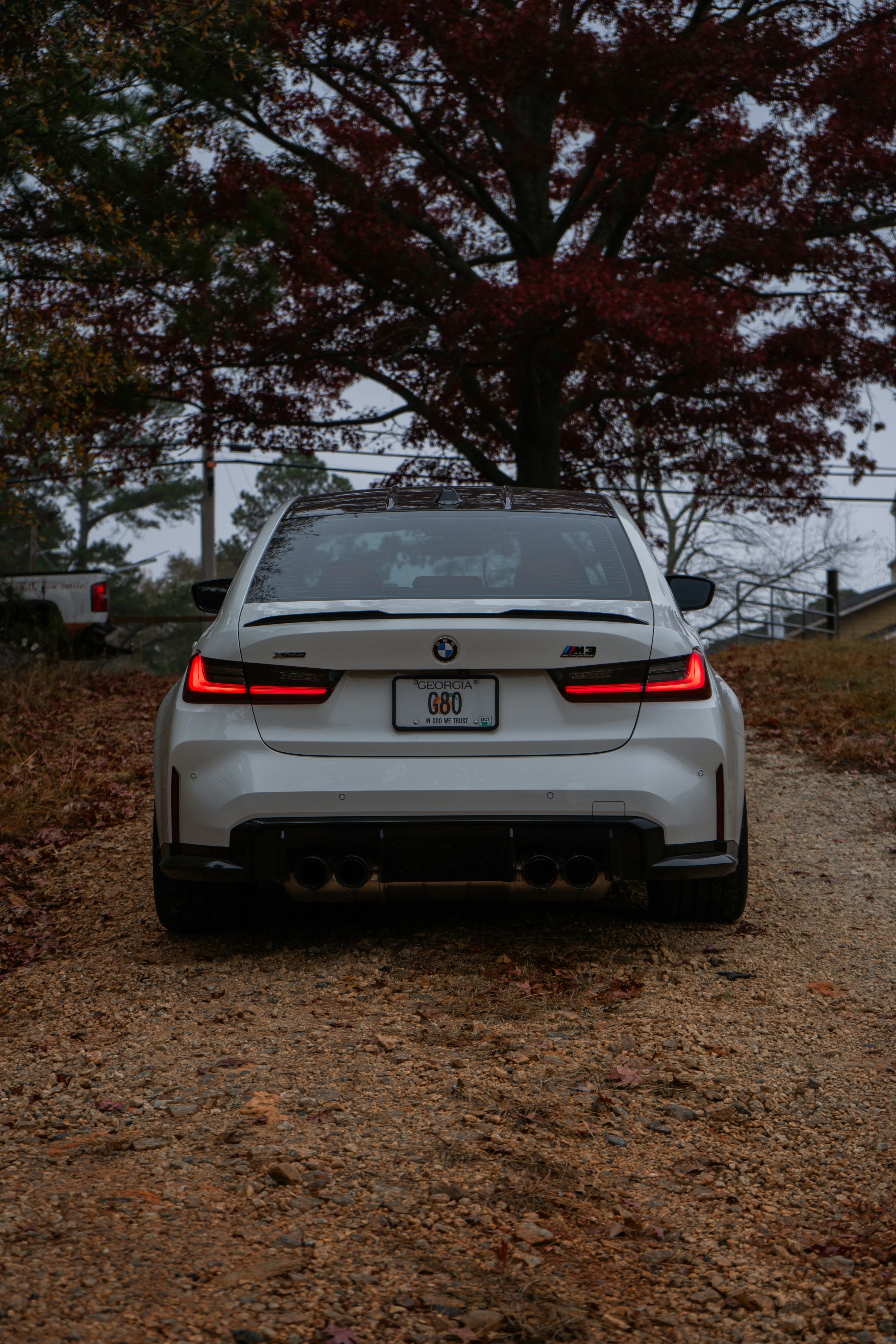 Tail-Lit Reverie: A White Sedan on a Leaf-Carpeted Gravel Road