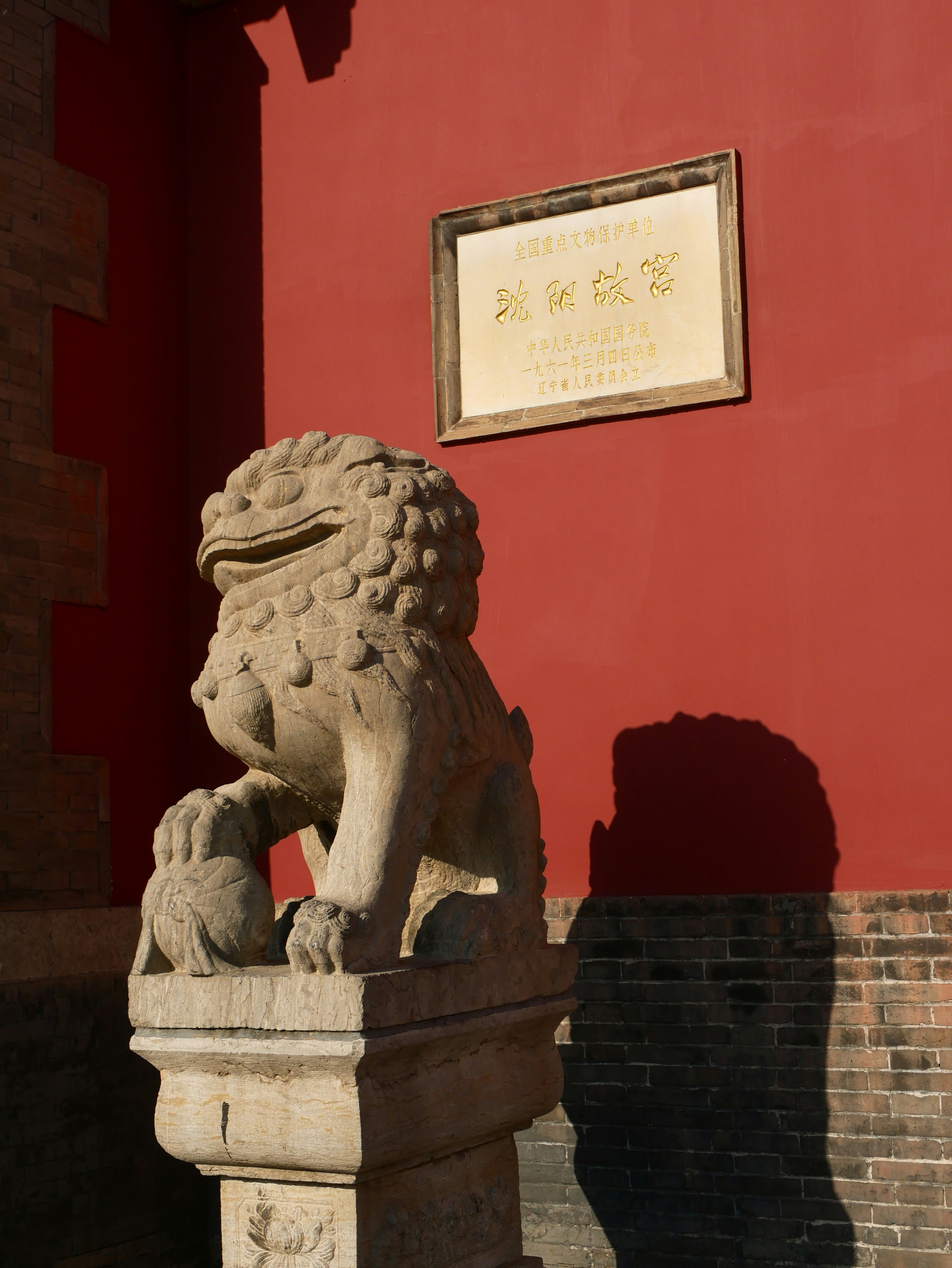 Crimson Sentinel: A Stone Guardian Framed by Sunlit Red Brick