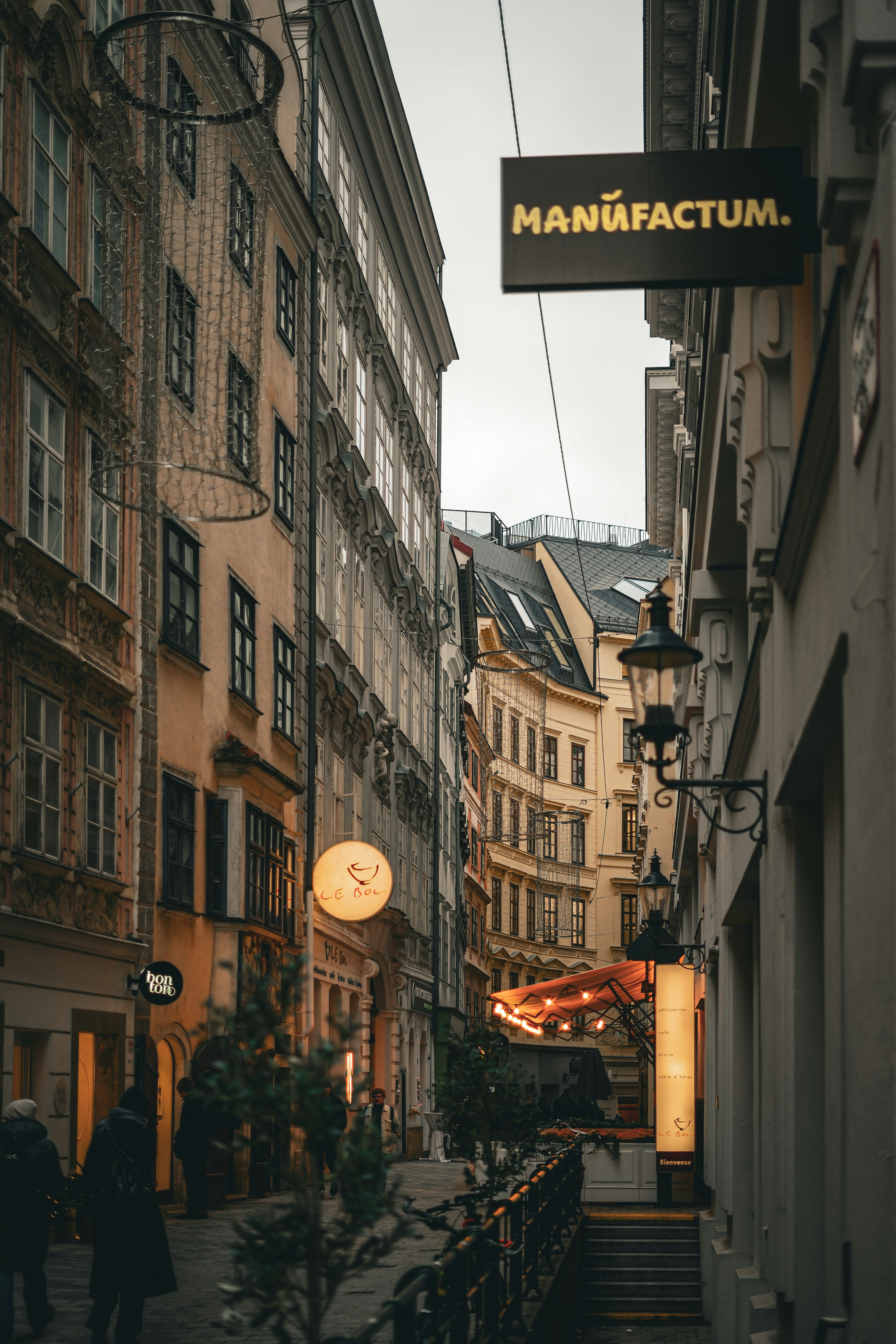 MANUFACTUM at Dusk: A Narrow European Alley Bathed in Lantern Light