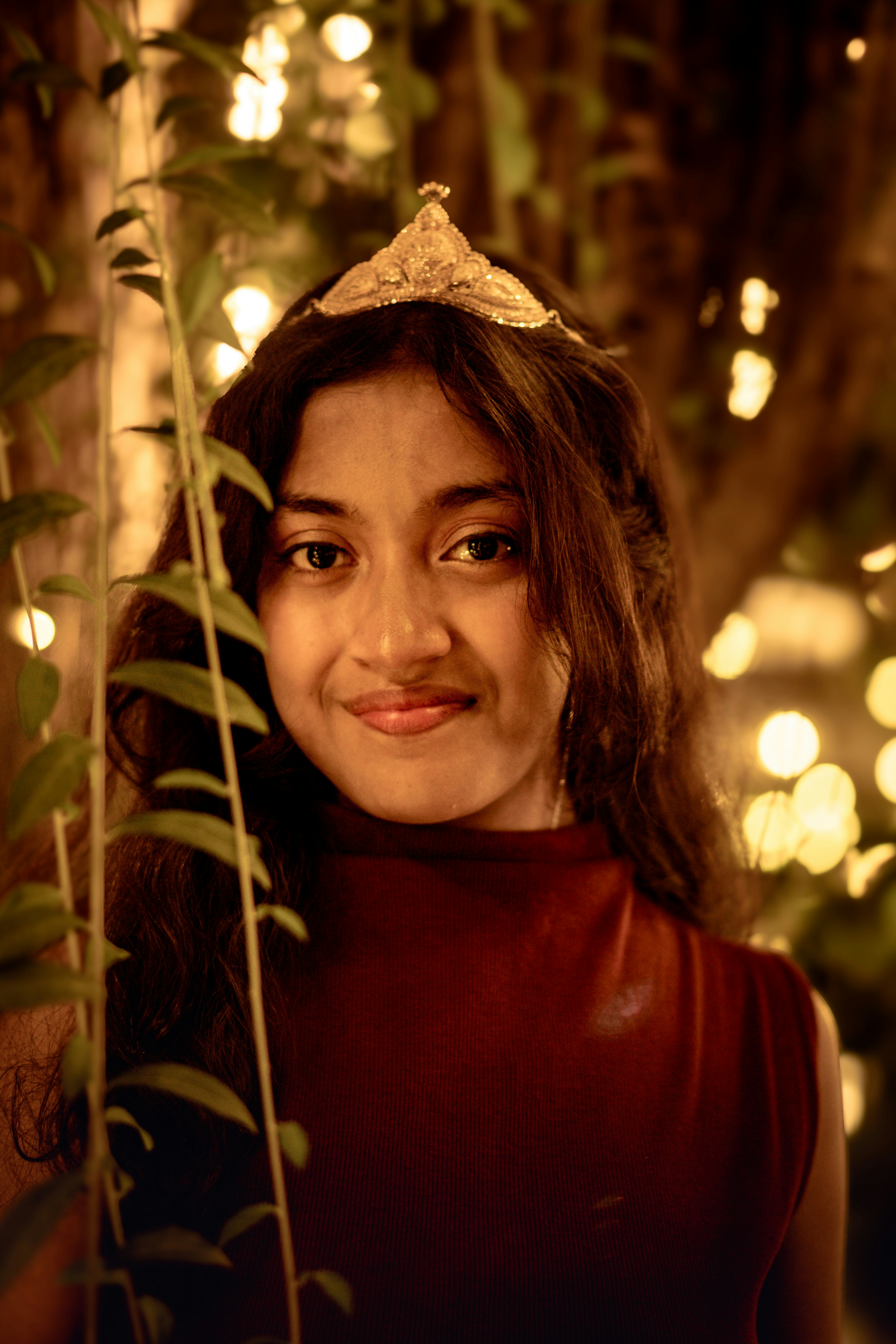 Velvet Light Portrait: A smiling girl in a tiara amid warm fairy-light glow