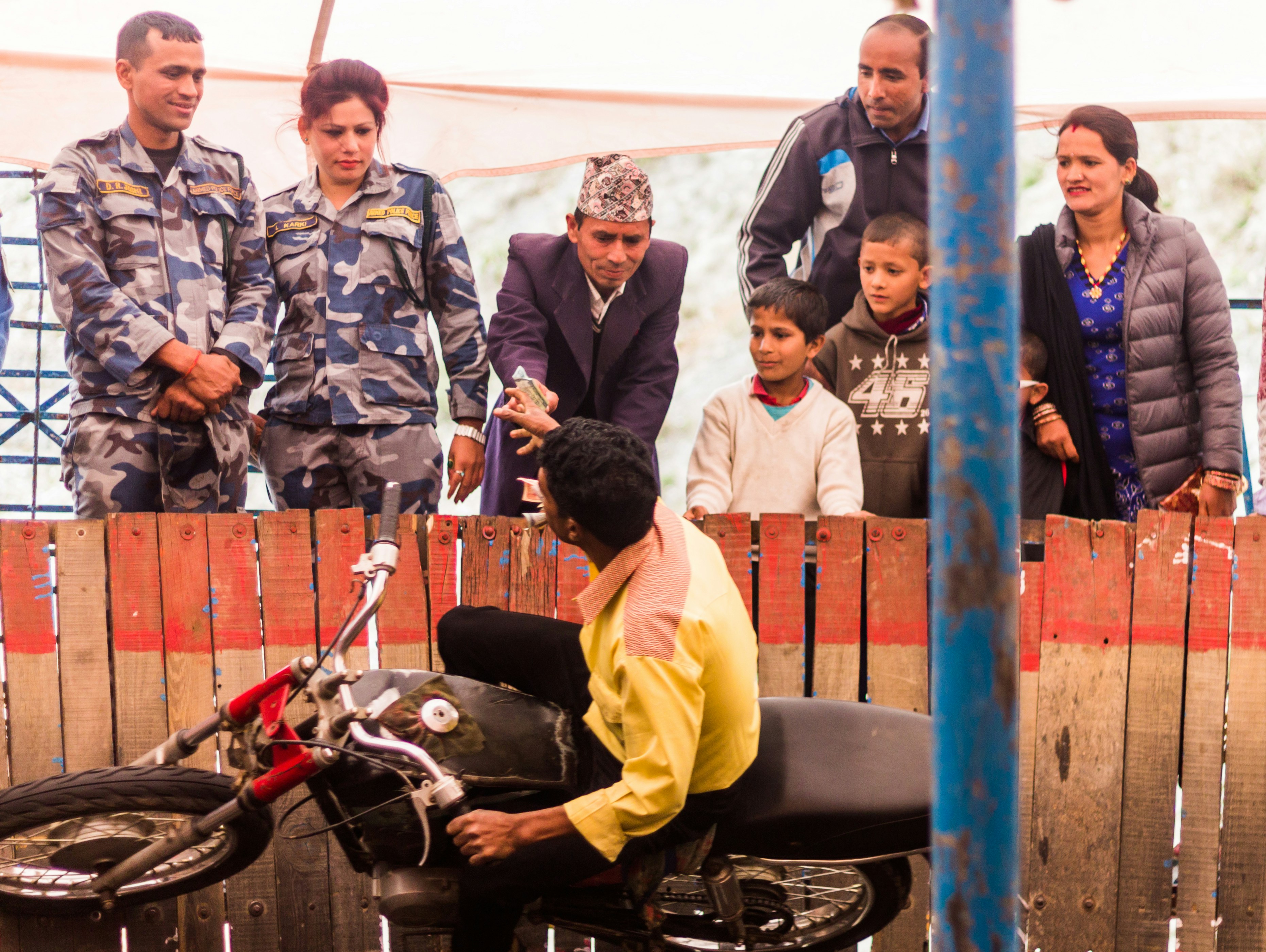 Yellow-Sleeve Resolve: A Rider Tends the Bike as Curious Onlookers Gather
