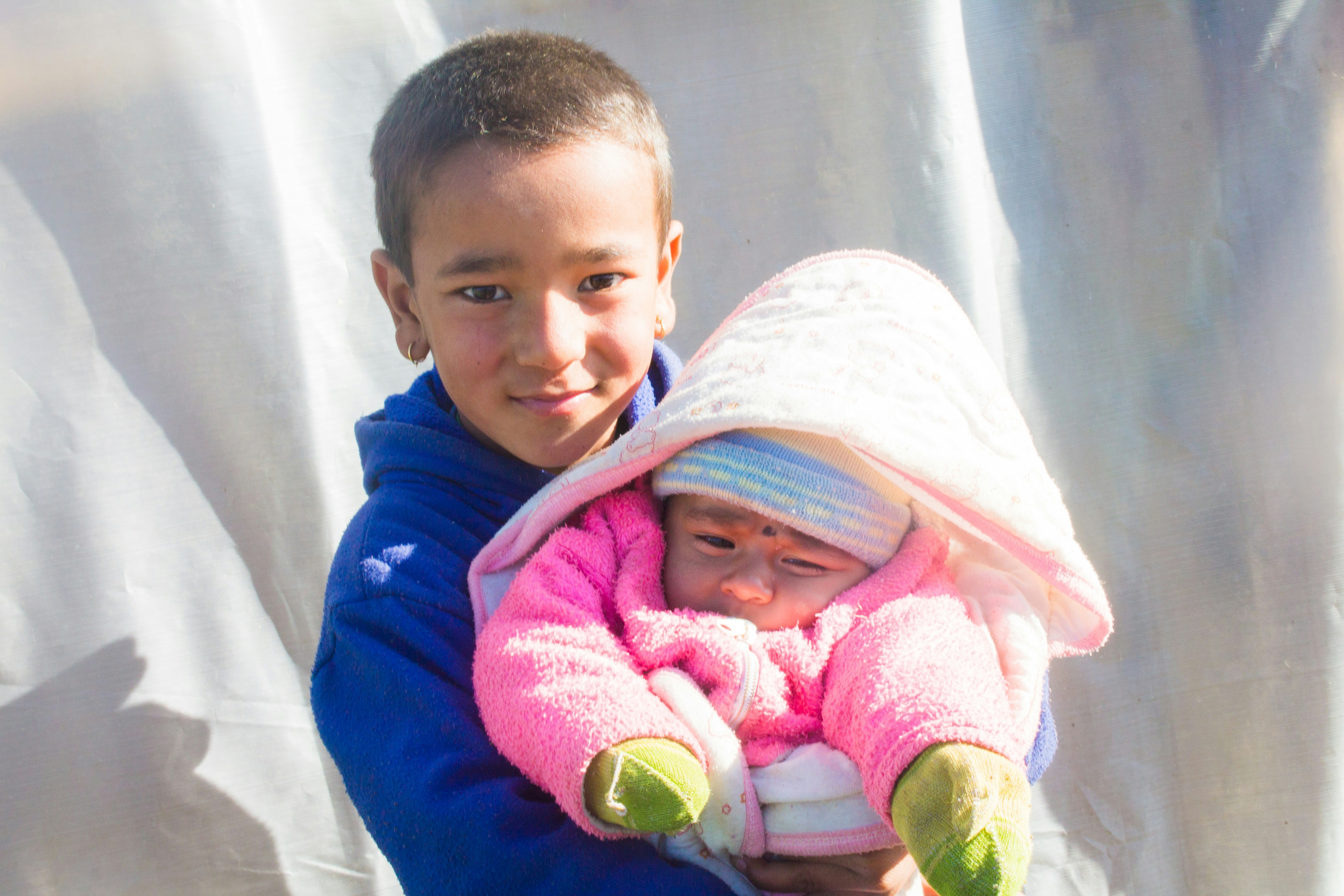 Sunlit Embrace: A Brother's Gentle Hold on a Baby in Bright Daylight