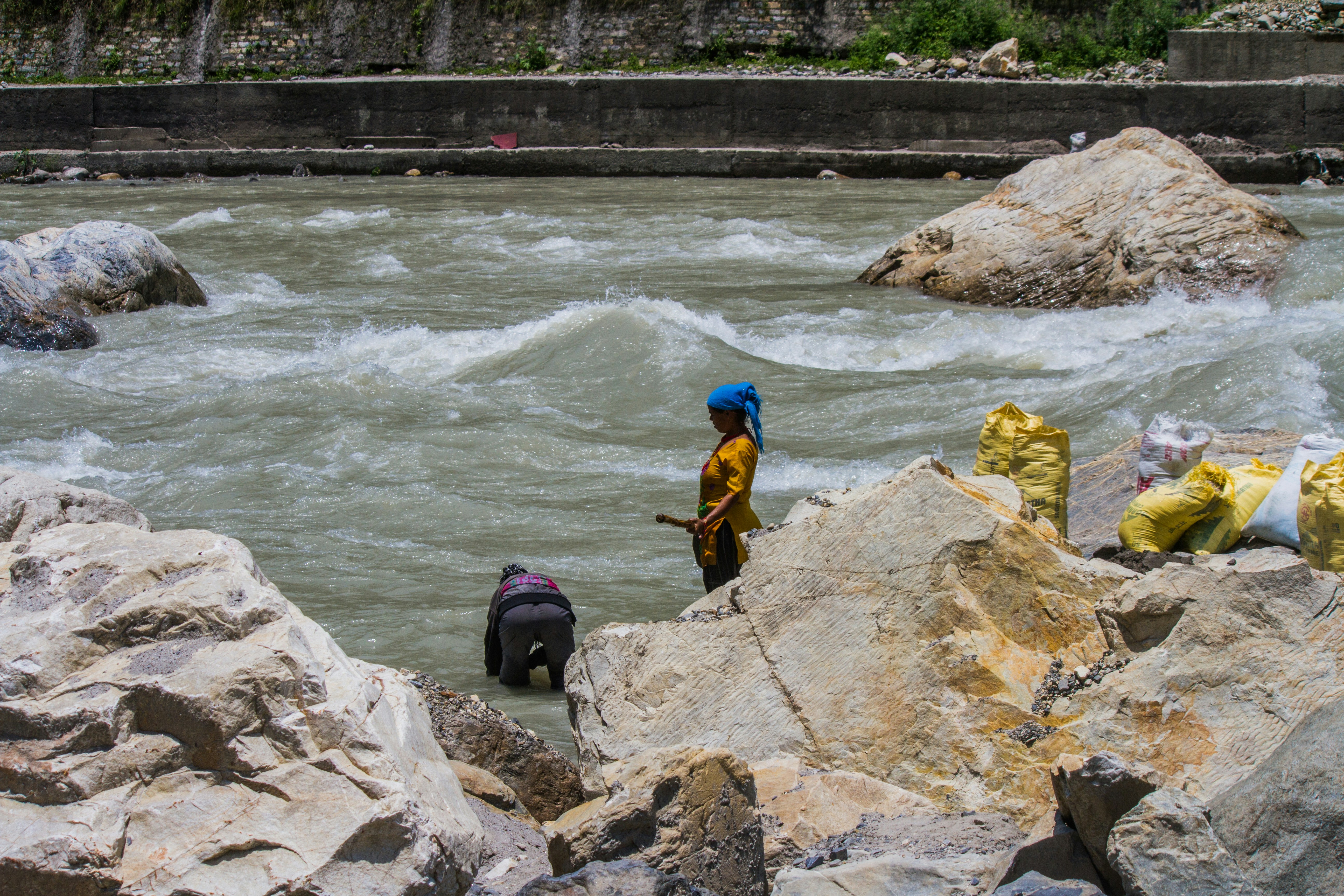 Blue-Turbaned Figure on the Riverbank Amid Rugged Rocks