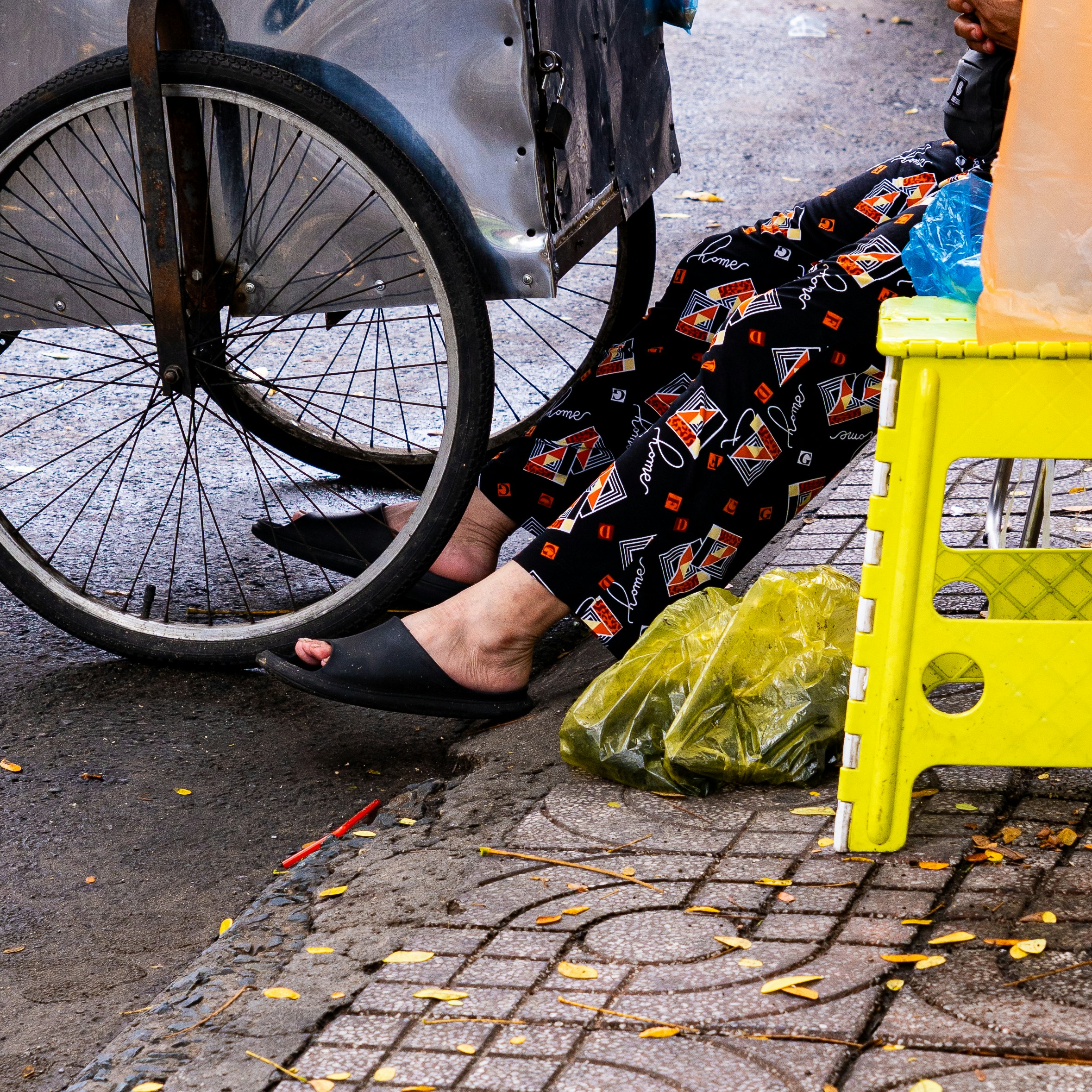 Under the Pedicab: Toes, Patterned Trousers, and a Yellow Crate