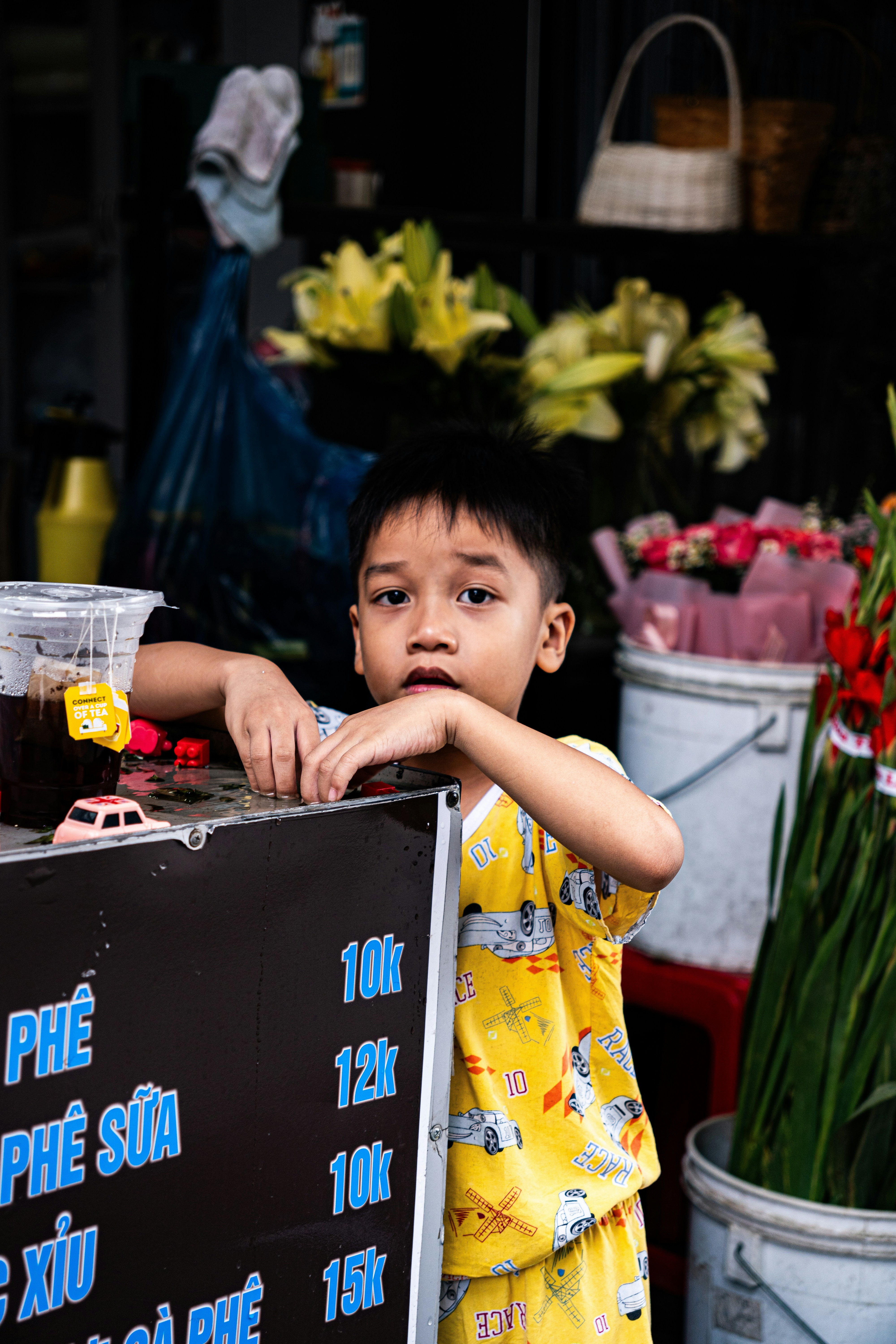 Market Moment: A Boy Pauses at a Flower Stall by the Price Board