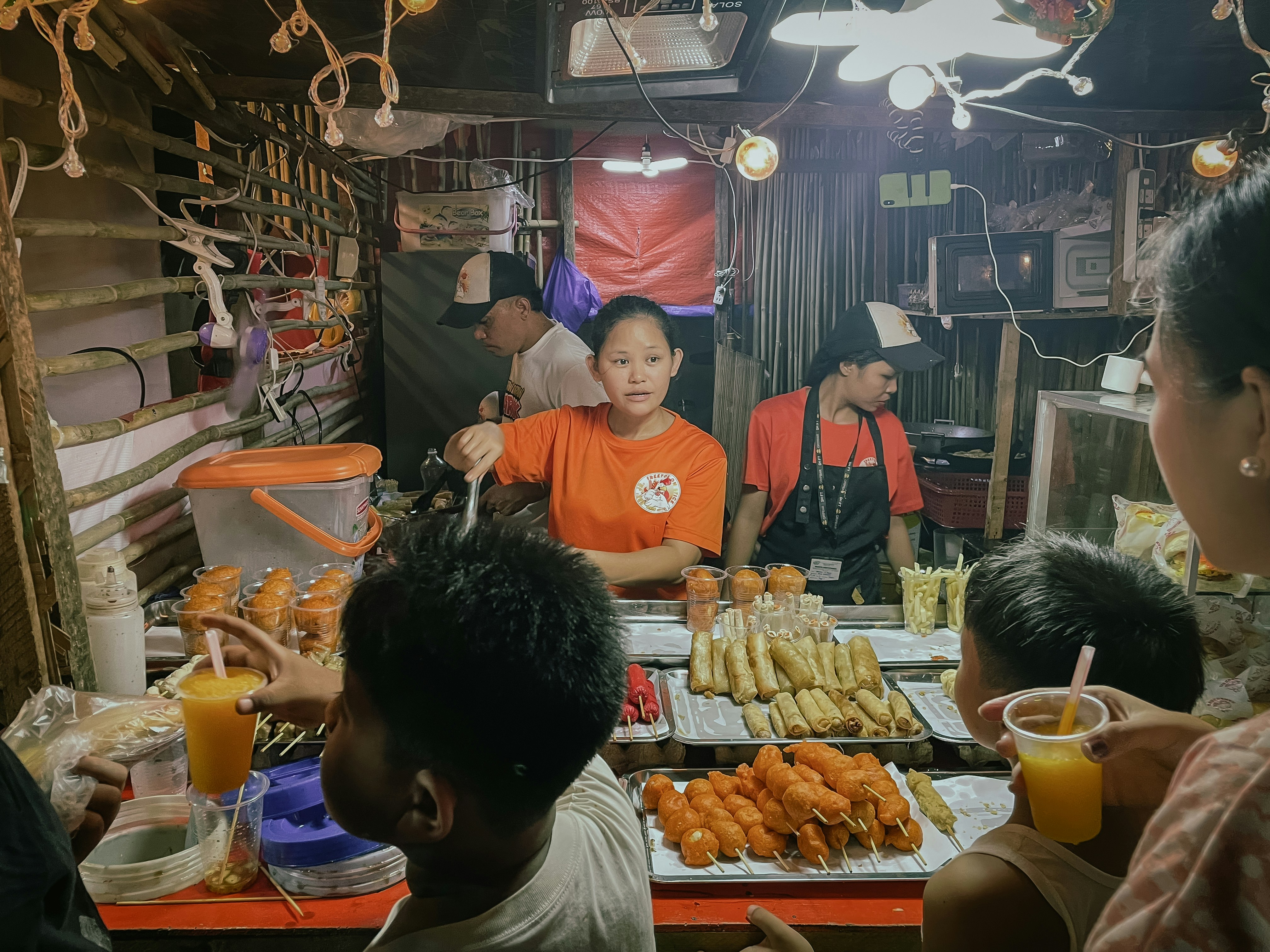 Center-Stage at a Busy Street-Food Stall: Orange-Shirt Vendor Oversees Skewers