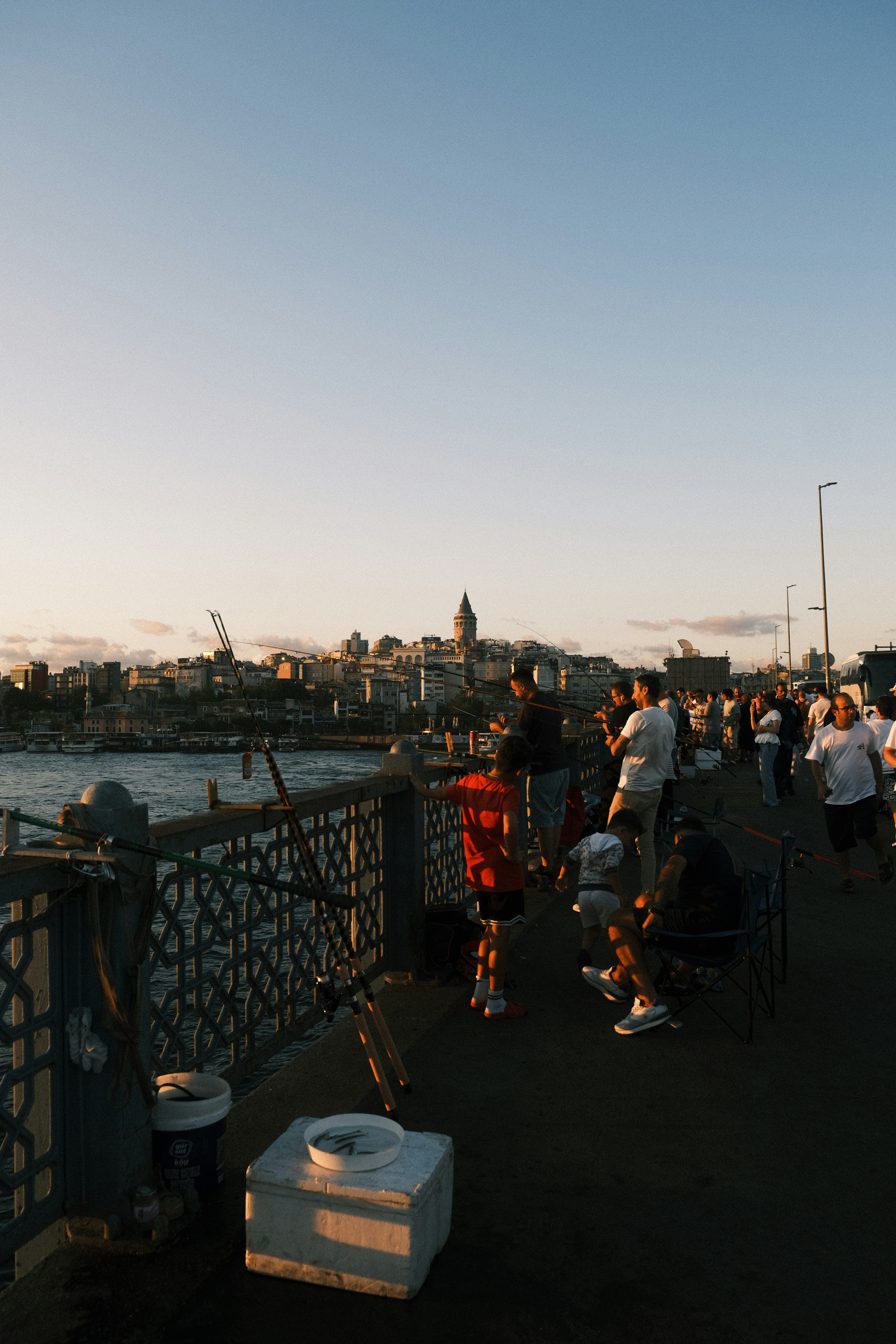 Red Shirt Angler at Sunset: A Crowded Riverside Scene with a Distant City Skyline