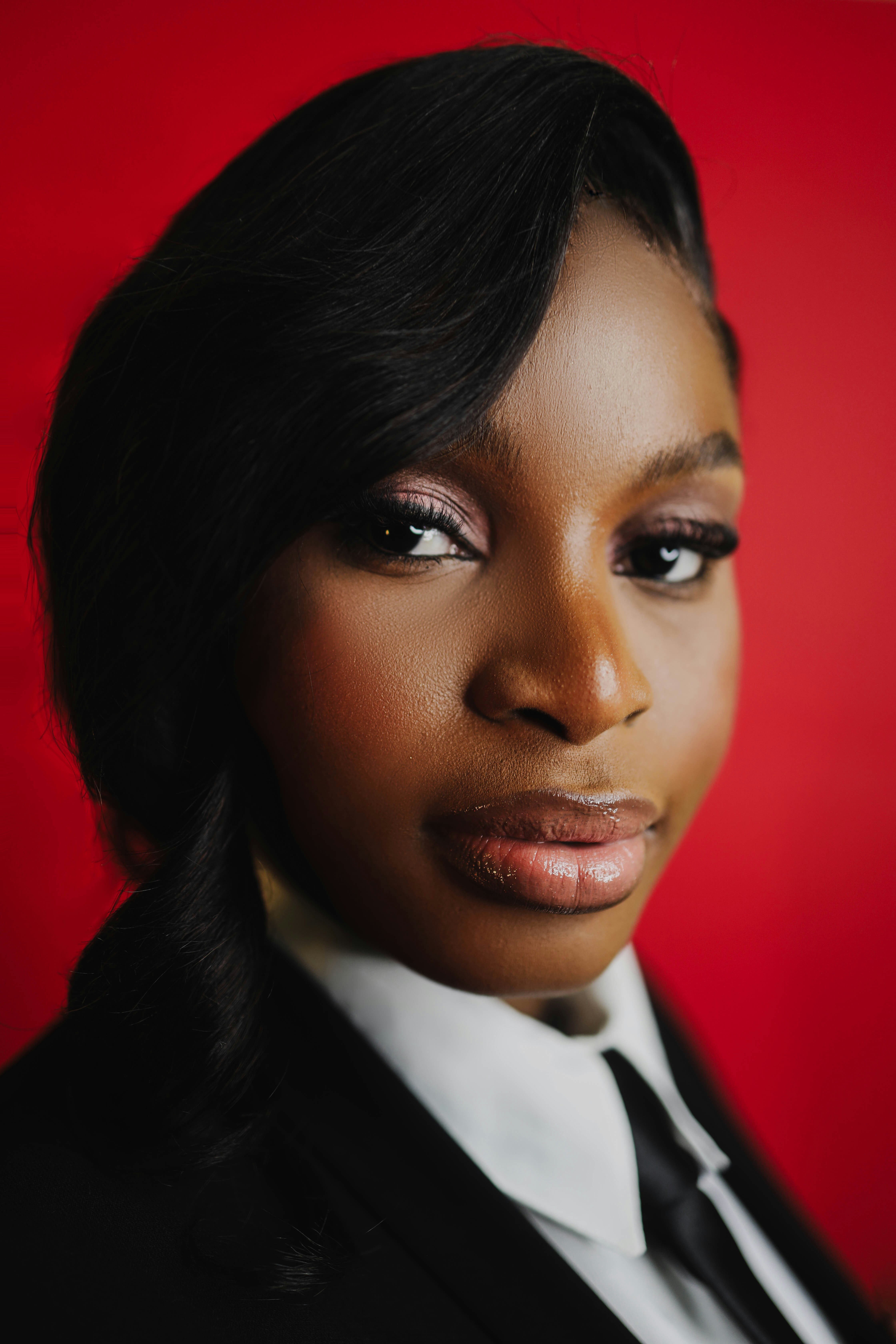 A stylish woman posing confidently in a black suit against a bright red background. Clean, bold, and modern vibes with a touch of attitude and elegance.