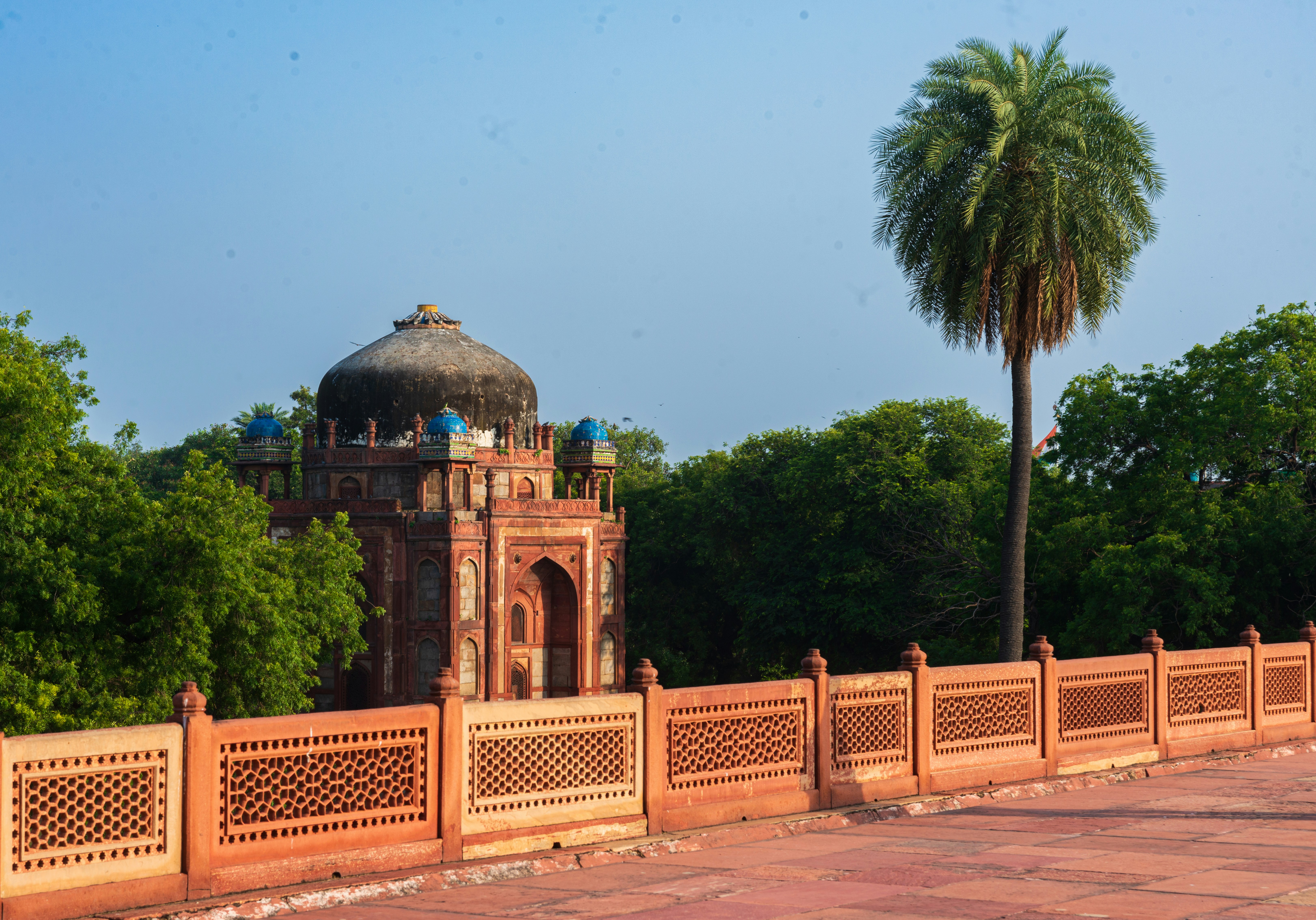 Located in the southeast quadrant of Humayun's Garden Tomb, the Barber's Tomb (Nai ka Gumbad) is a striking red and gray sandstone mausoleum. Standing on a square plinth, the symmetrical structure features four corner chhatris and a central dome resting on an octagonal drum. The design mirrors the main tomb’s grandeur, utilizing squinch arches, intricate geometric jali screens, and star-shaped spandrel decorations. Notable details include a stone mihrab with a Sultanate-style hanging-bell motif. Inside, two anonymous cenotaphs rest beneath the high dome.