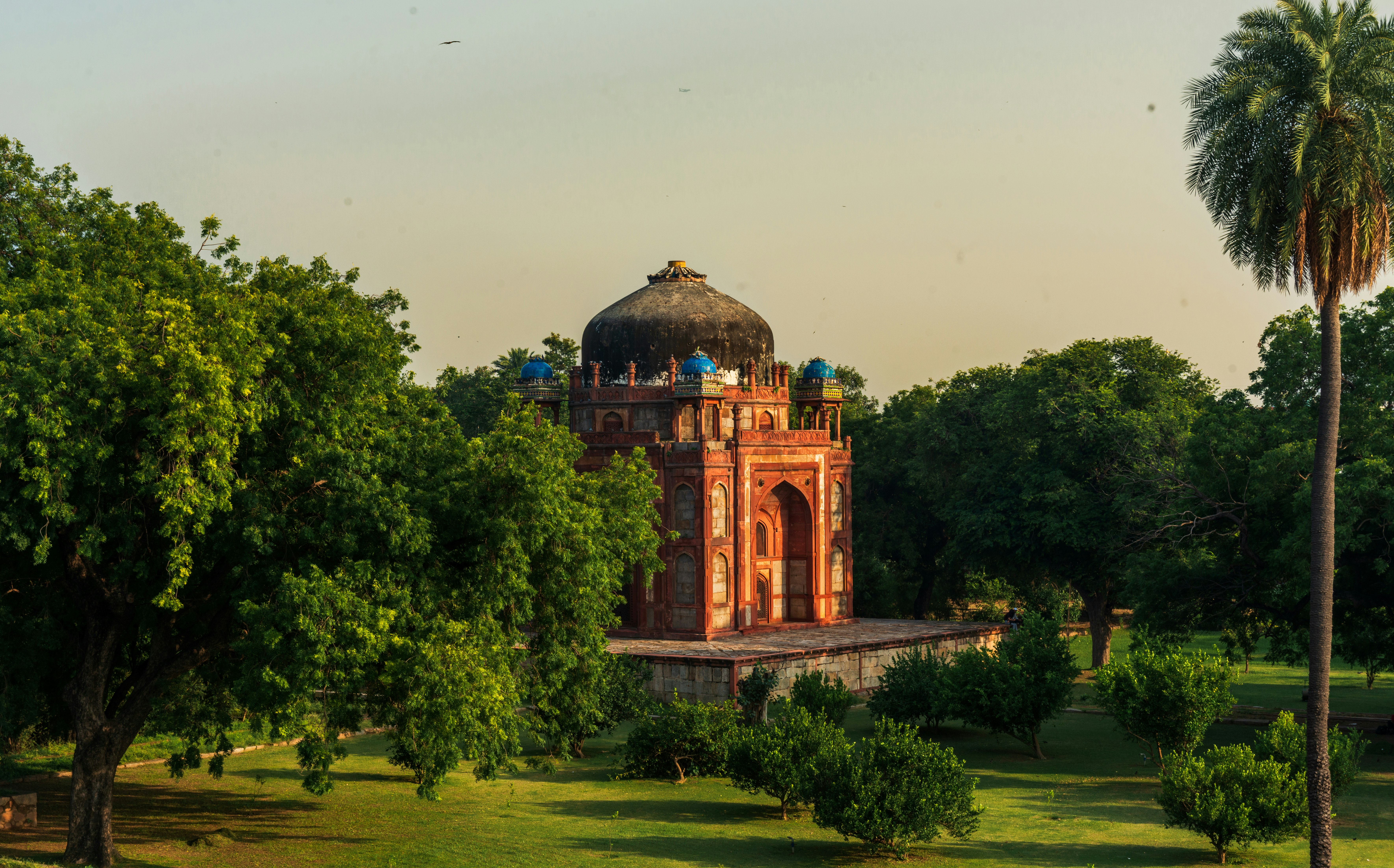 Located in the southeast quadrant of Humayun's Garden Tomb, the Barber's Tomb (Nai ka Gumbad) is a striking red and gray sandstone mausoleum. Standing on a square plinth, the symmetrical structure features four corner chhatris and a central dome resting on an octagonal drum. The design mirrors the main tomb’s grandeur, utilizing squinch arches, intricate geometric jali screens, and star-shaped spandrel decorations. Notable details include a stone mihrab with a Sultanate-style hanging-bell motif. Inside, two anonymous cenotaphs rest beneath the high dome.