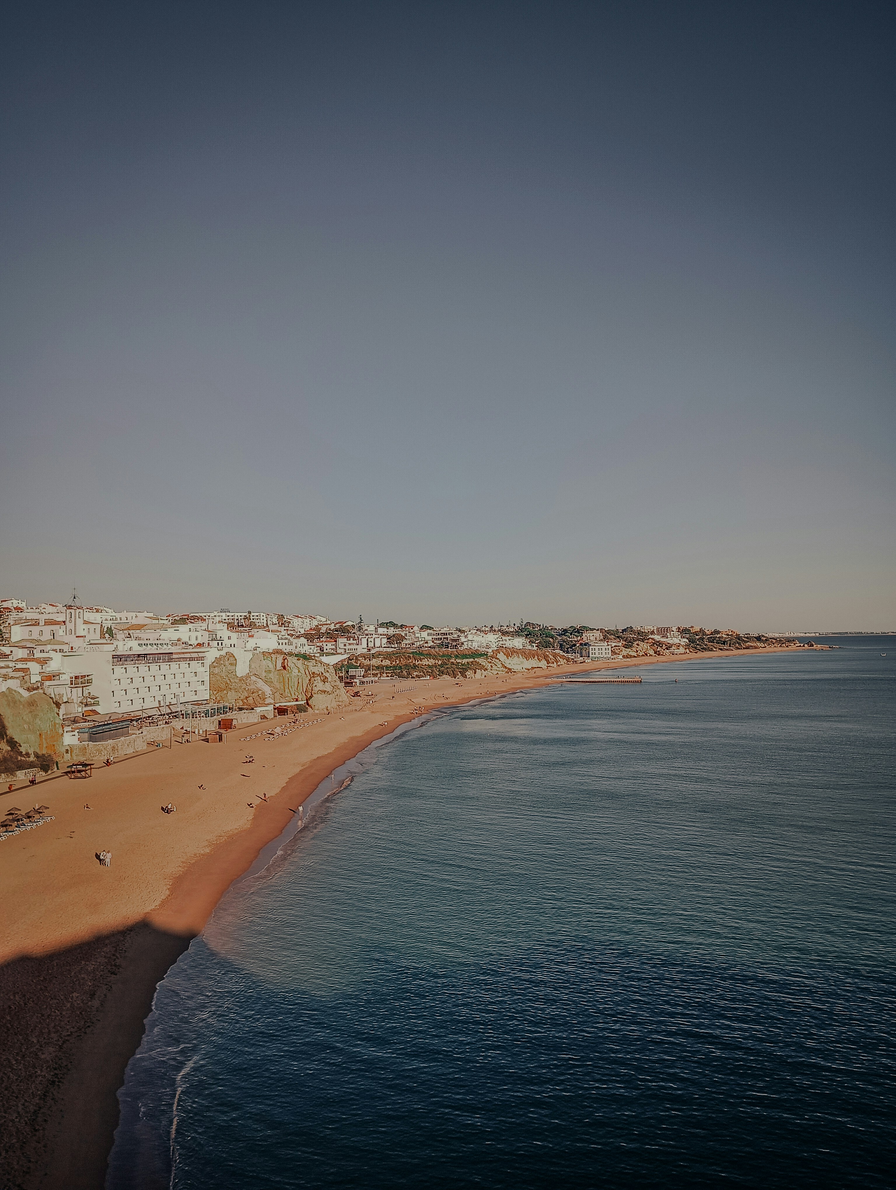 Beach with calm ocean and distant buildings.