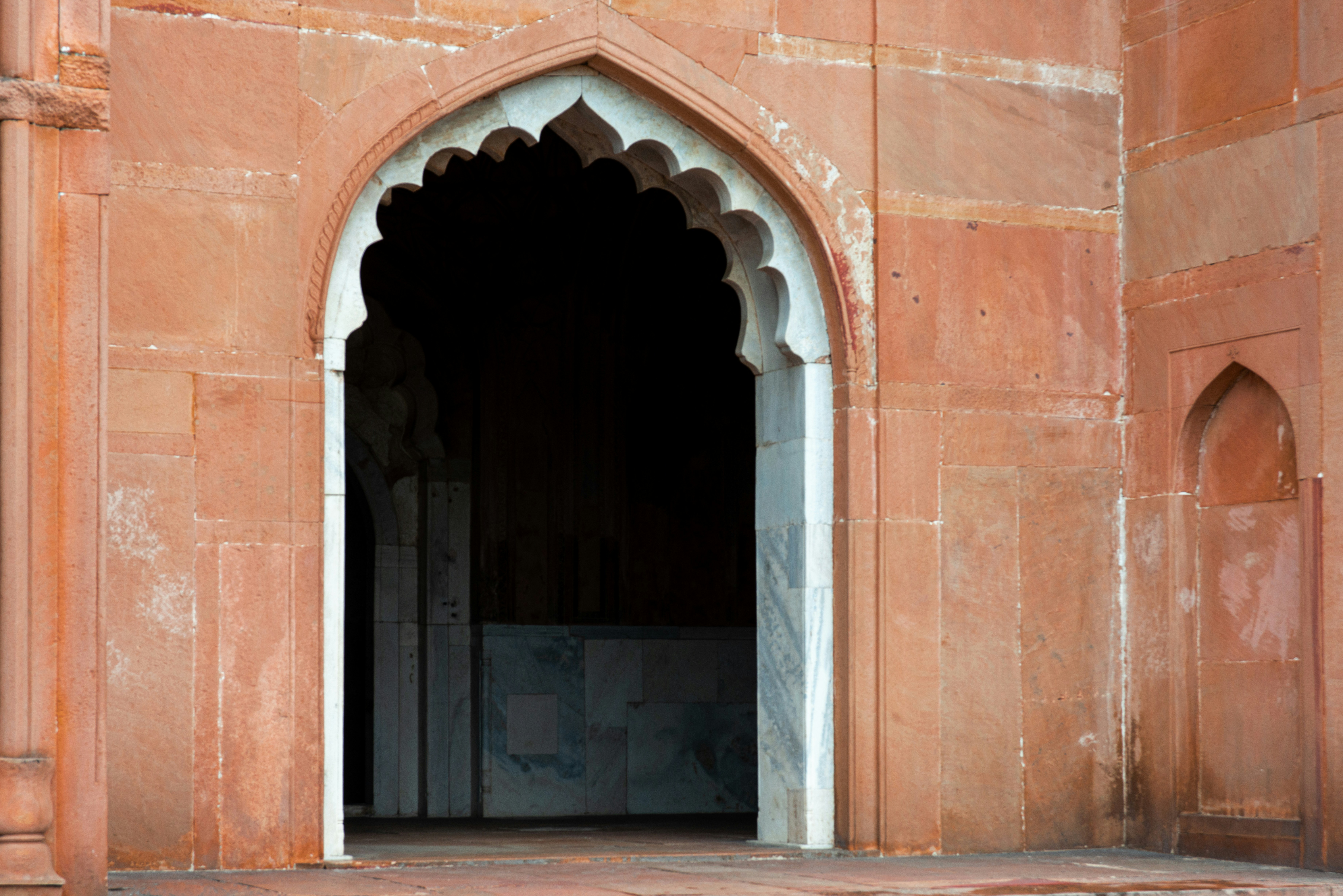 A sandstone Mughal style archway with a scalloped marble frame that opens into a dark interior corridor at Safdarjung’s Tomb in Delhi.